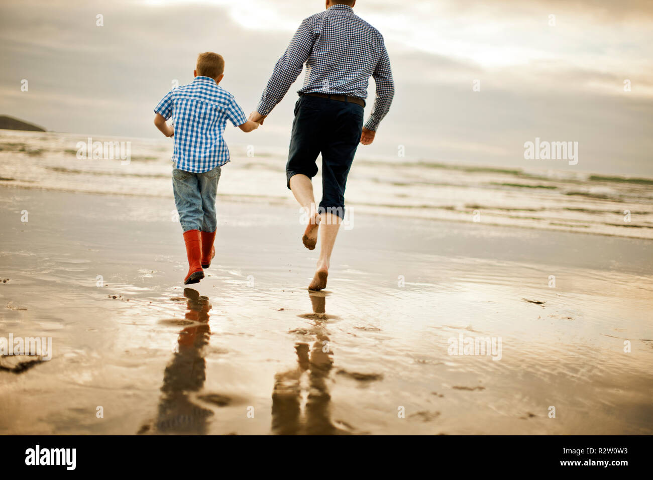 Mid-adult man running hand in hand with his son on the back Stock Photo ...