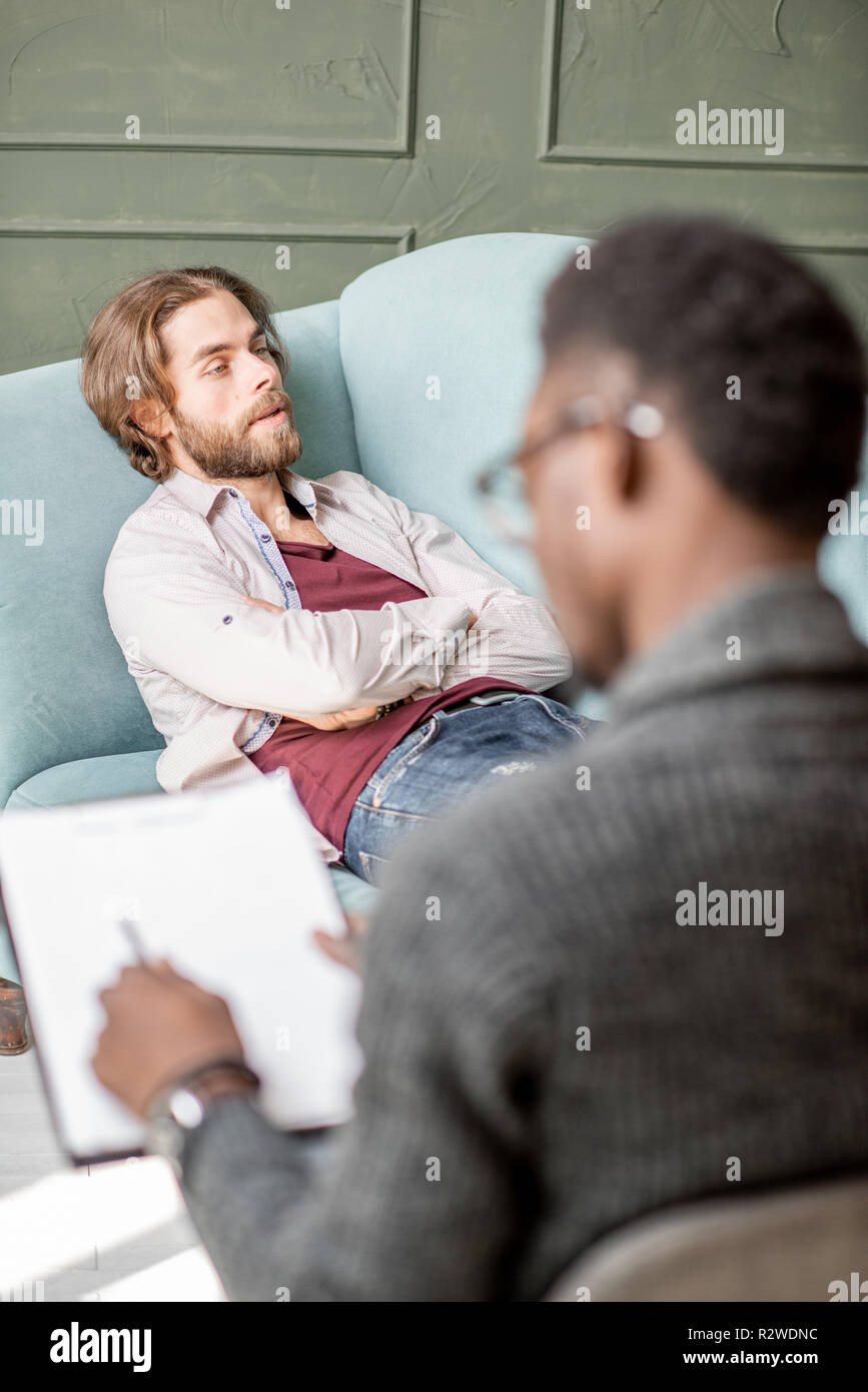 Young caucasian man visiting an african psychologist lying on the ...