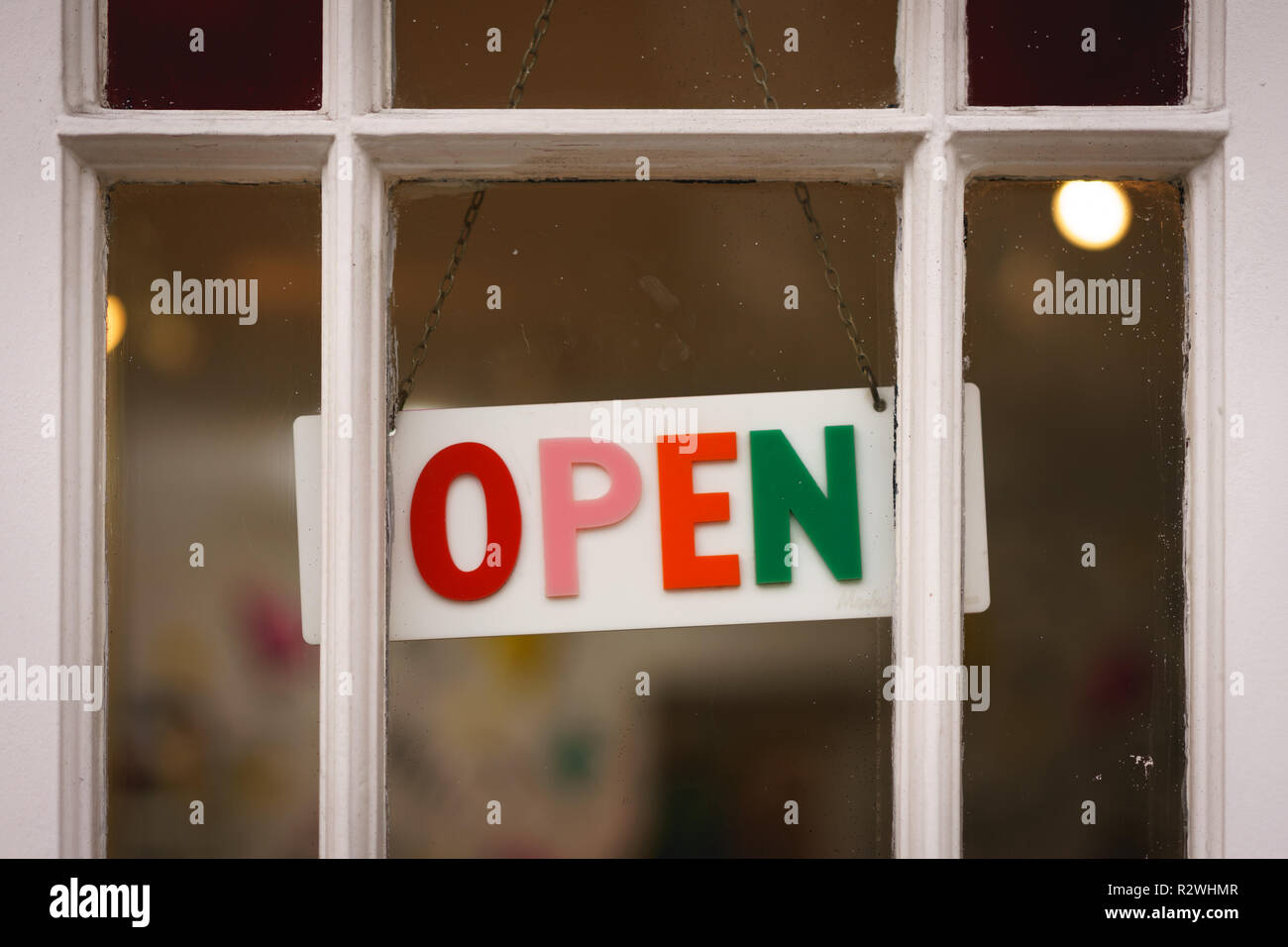 Open signboard with coloured letters on a shop door with a white wooden ...