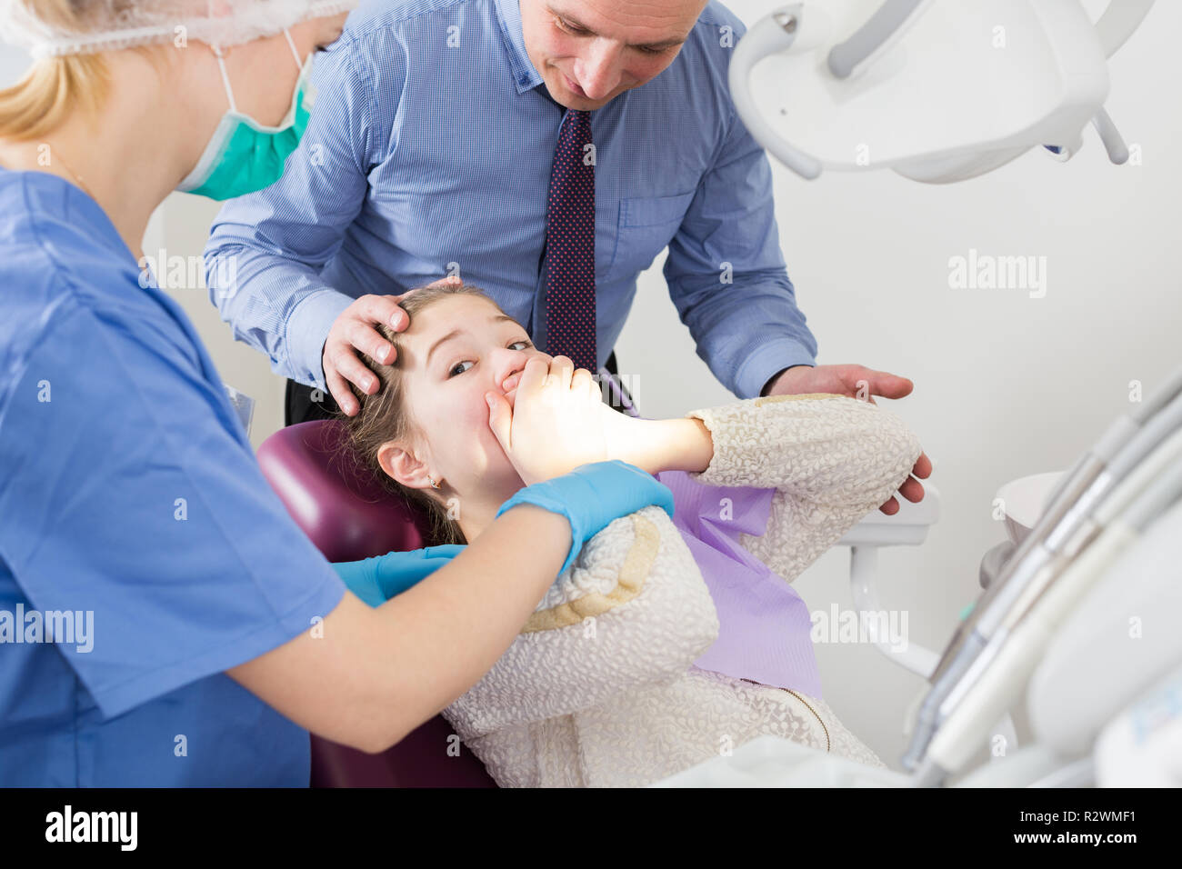 Frightened girl in dental chair refusing to open mouth while father supporting her Stock Photo ...