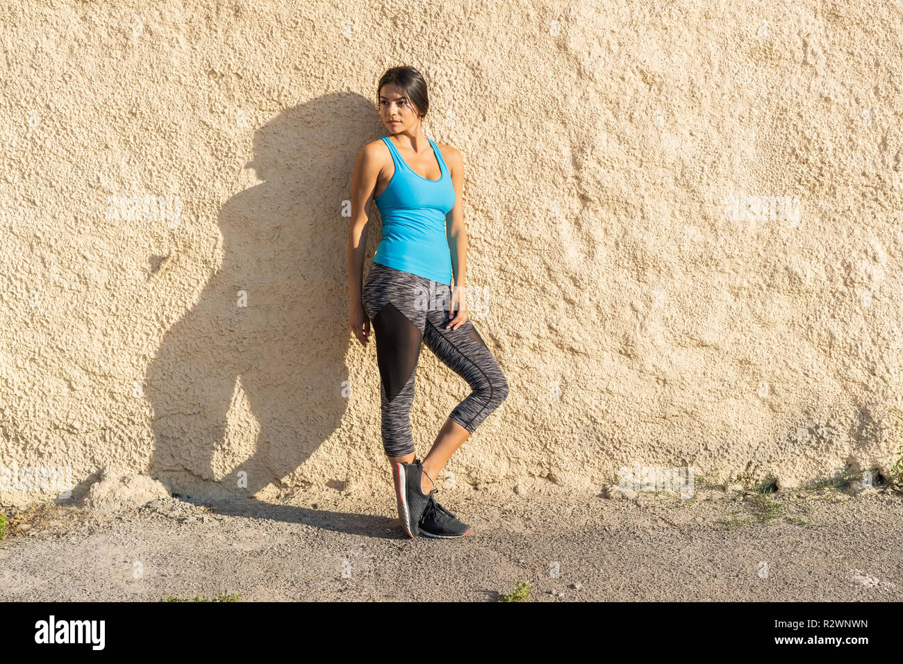Shot of fit runner standing against a wall outdoors. Sporty woman ...
