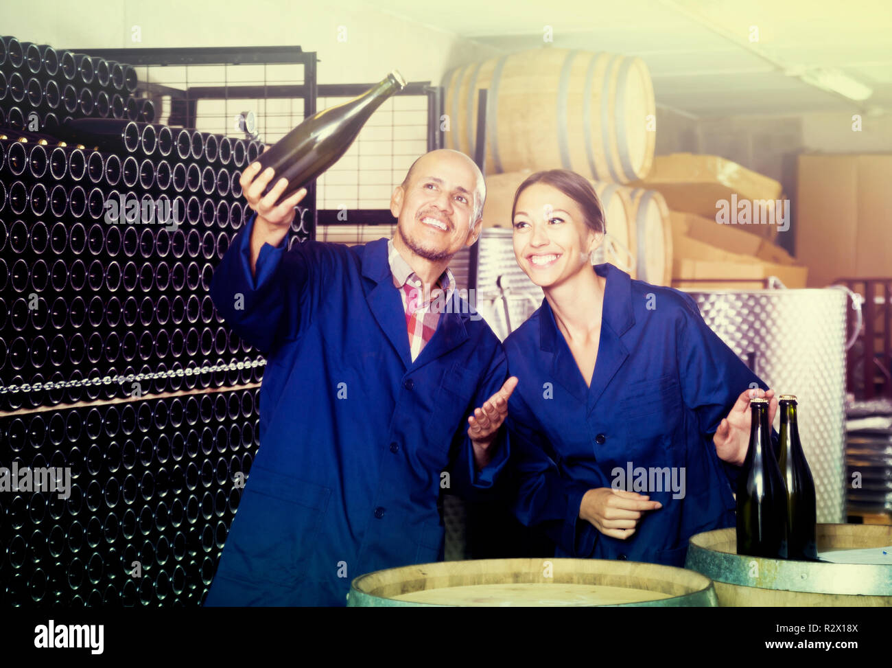 cheerful man and women winemakers looking on bottle of sparkling wine ...