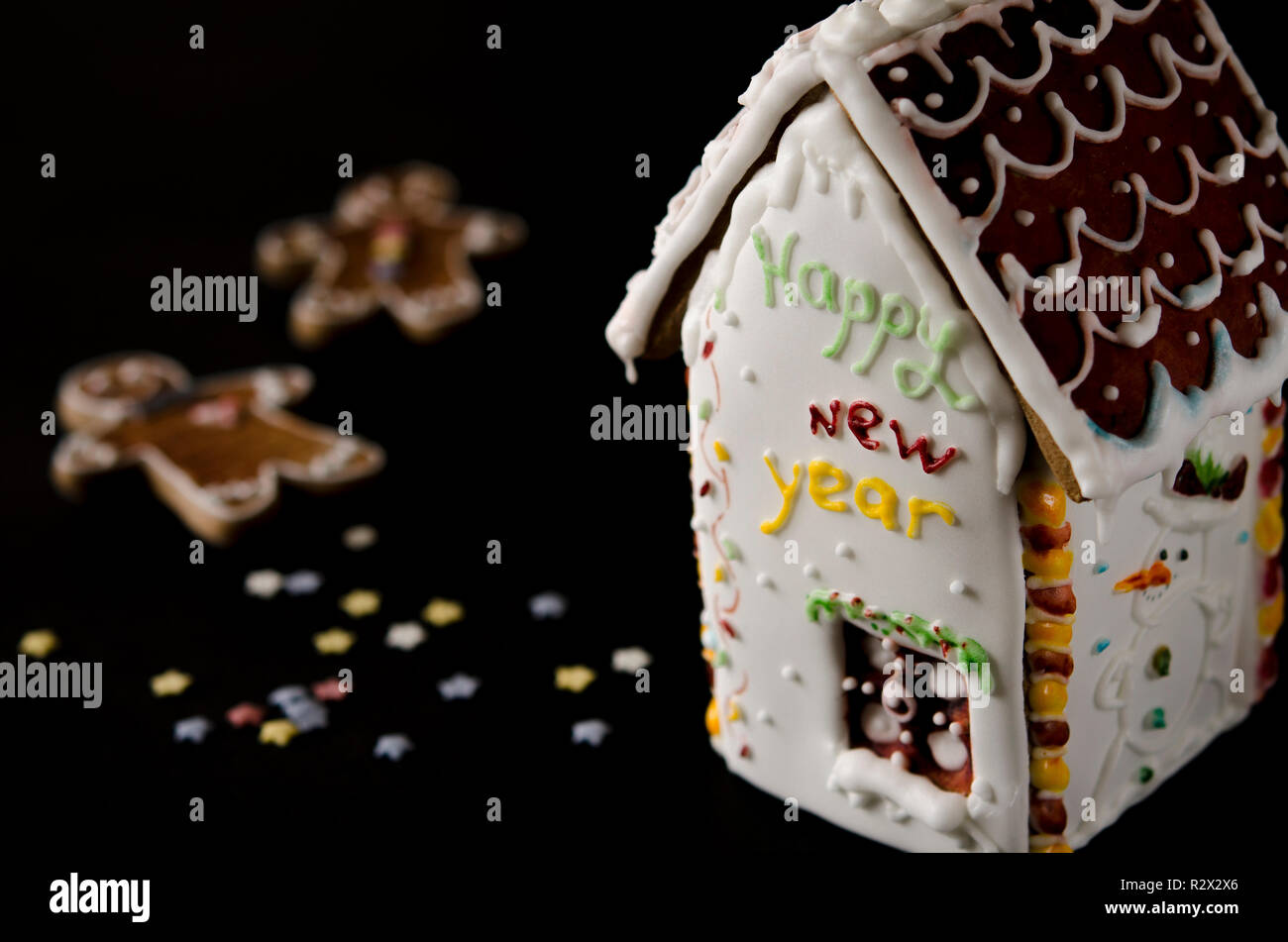 On a black background is a white gingerbread house with a brown roof, a ...