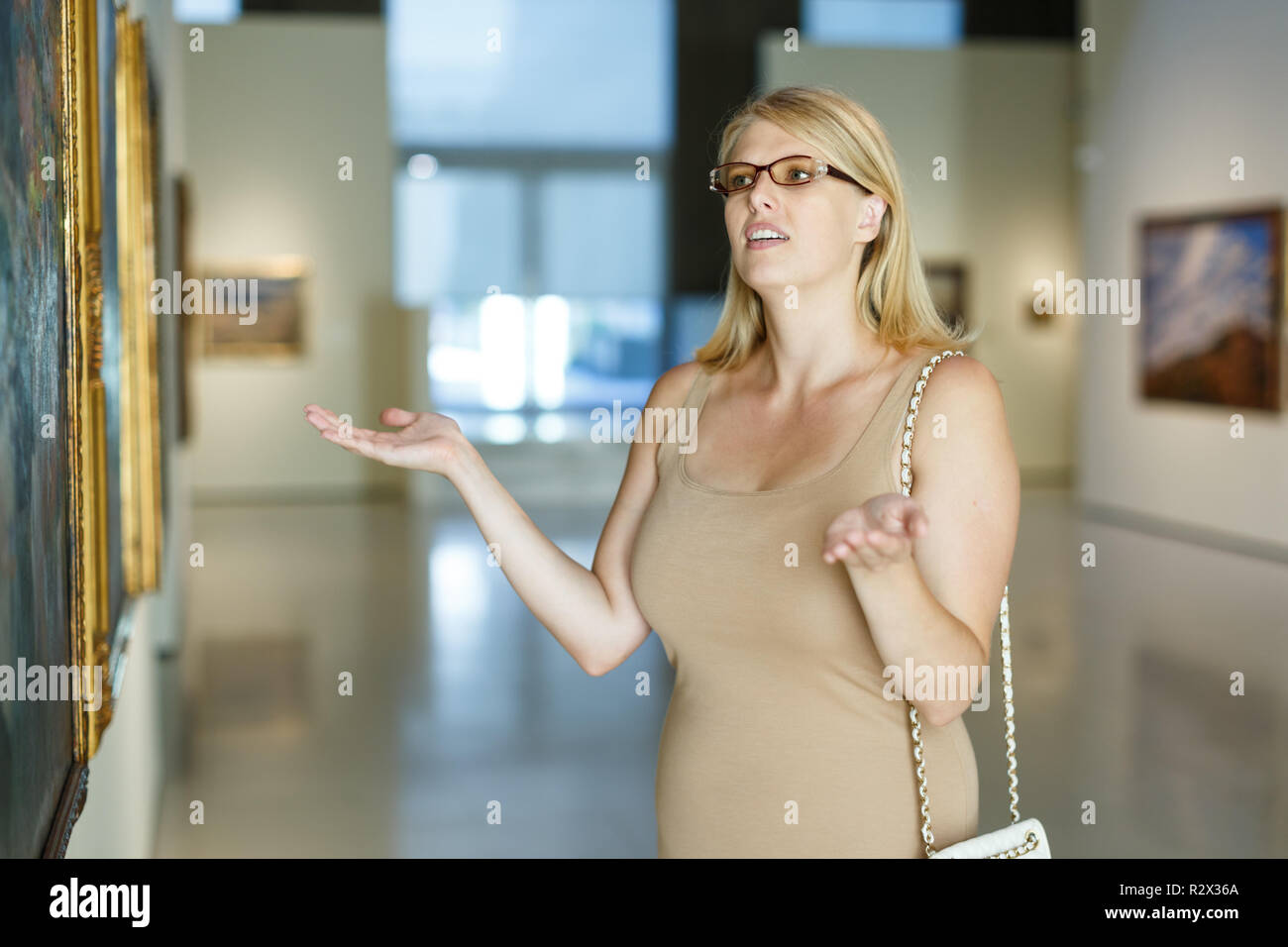 Woman wearing glasses throwing up her hands near the picture in art ...