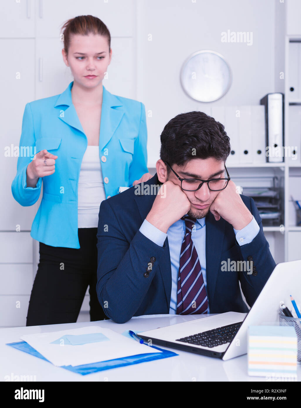 Upset man sitting at laptop with disgruntled female boss behind Stock ...