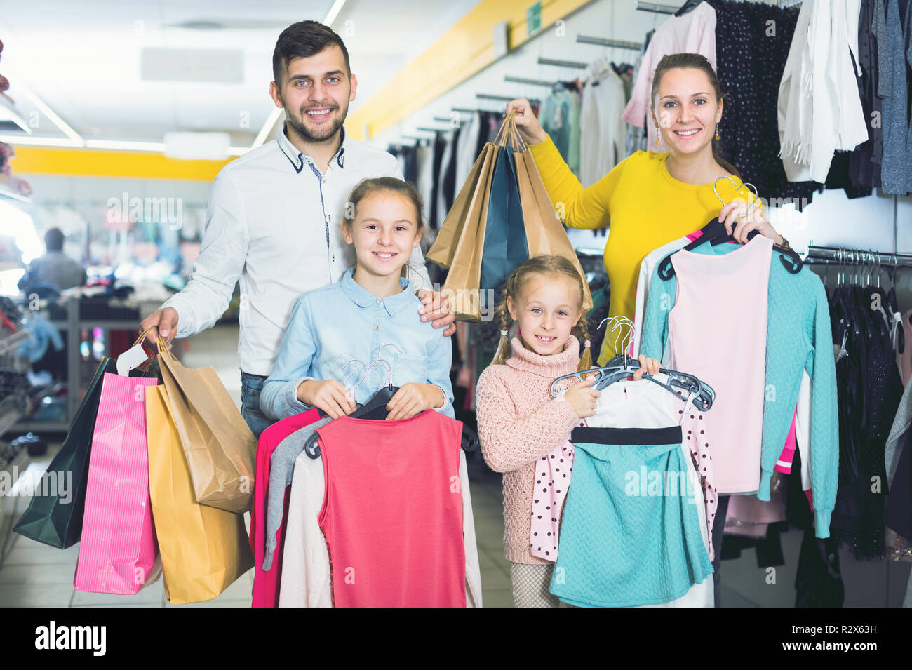 Young positive family with two daughters after shopping in clothes shop ...