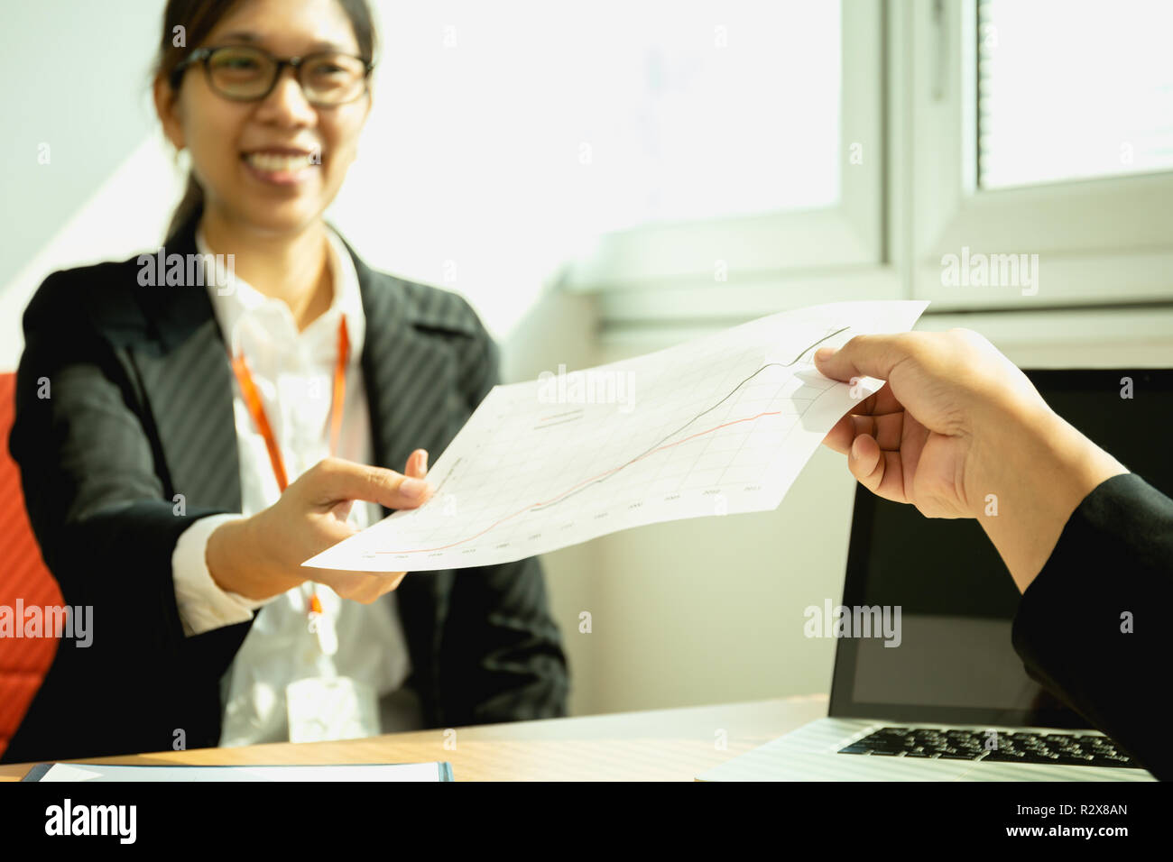 Businessman working at office desk with laptop handing paper chart to ...