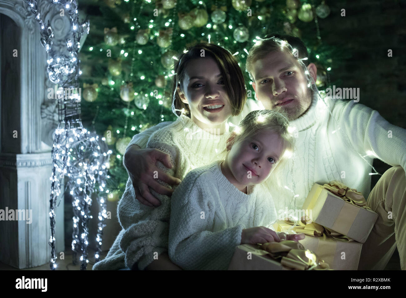 Happy family wrapped in a garland sits near a Christmas tree. New year ...