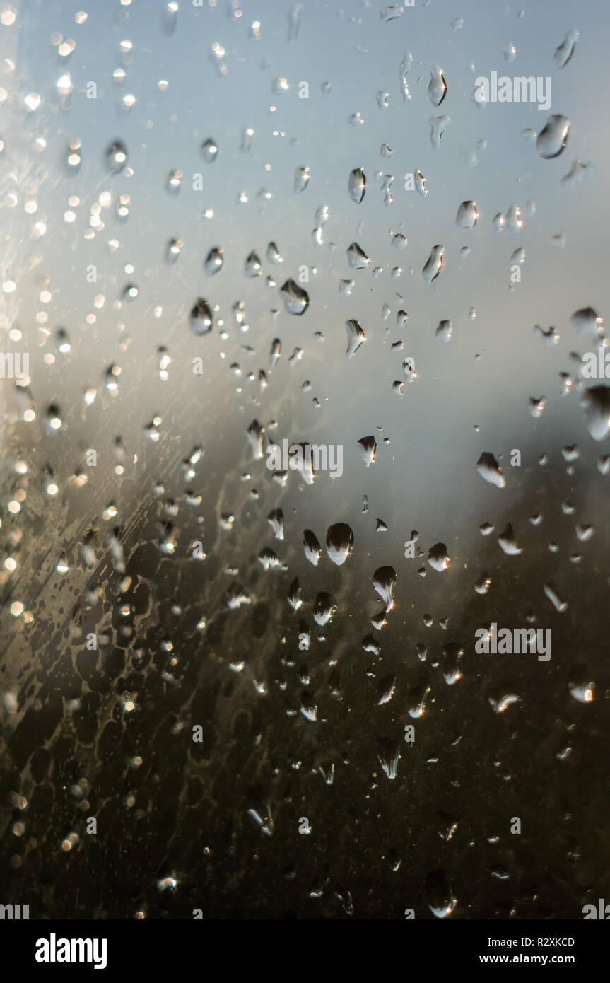 raindrops on window glass on background of cloudy sky and landscape ...