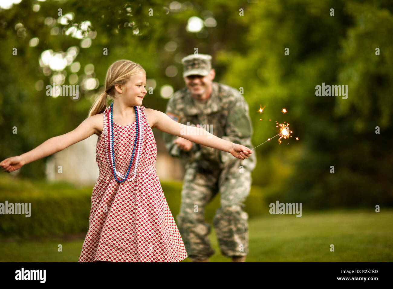 Young girl dancing with sparklers in the back yard with her father ...