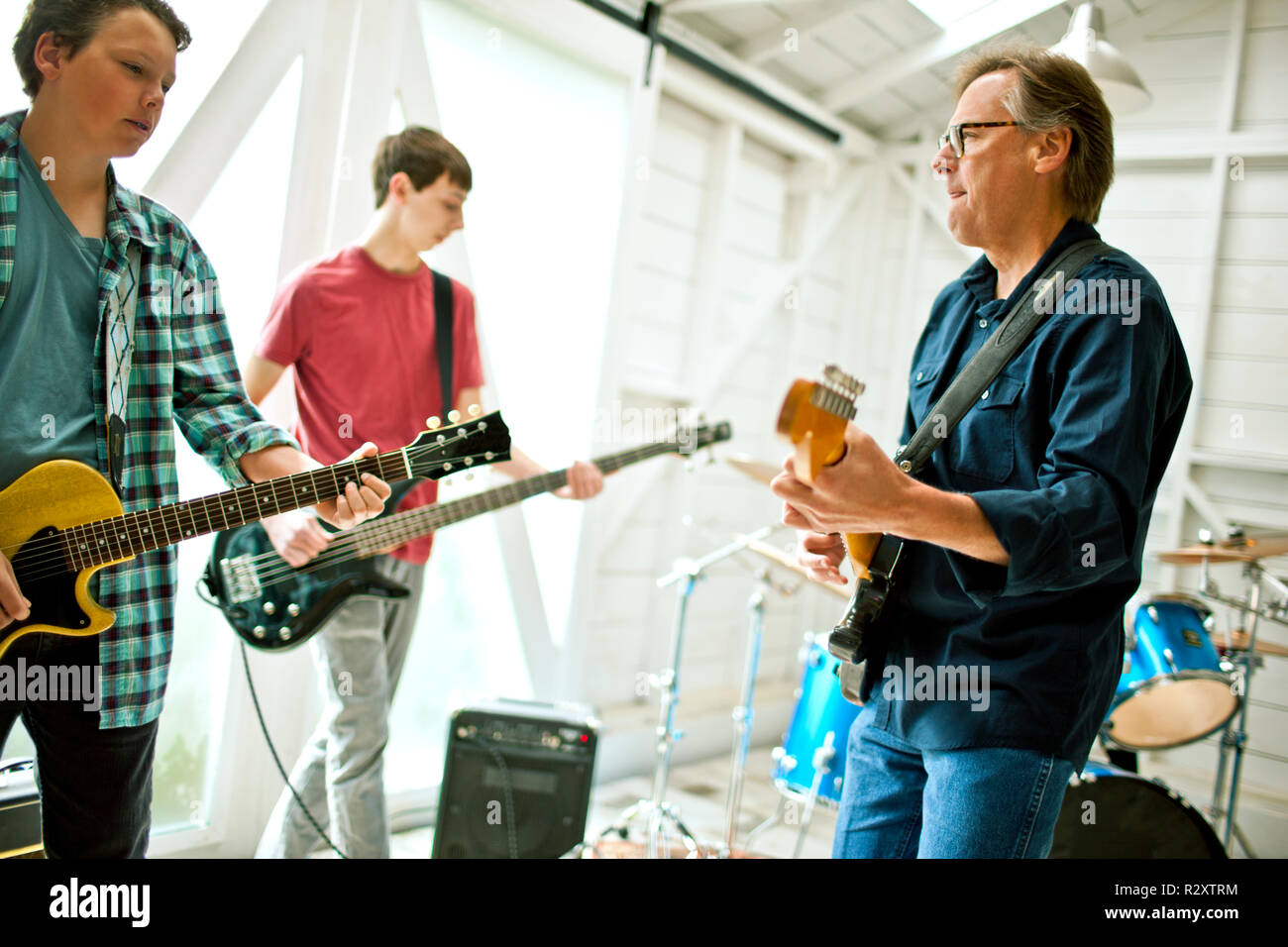 Mid adult man and two teenage boys playing guitars together inside a ...