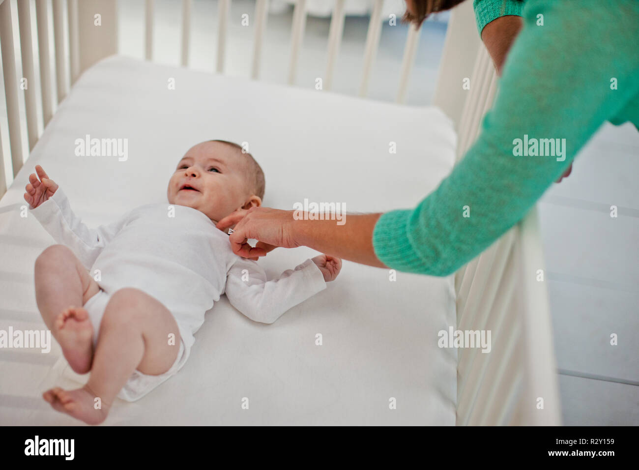 Young mother gently tickling her smiling baby boy's neck as he lies in ...