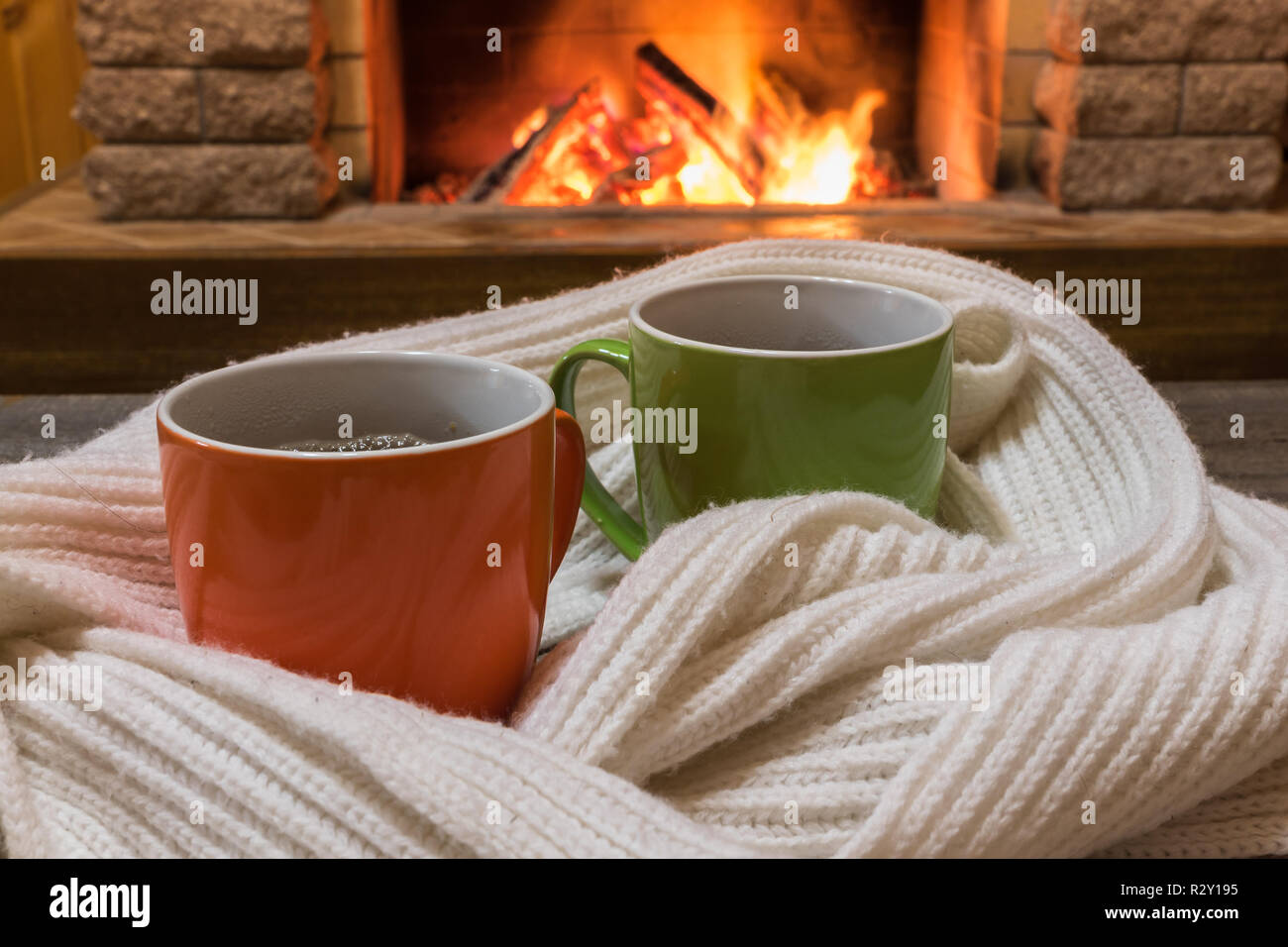Two mugs with hot tea and cozy warm scarf near fireplace, in country ...