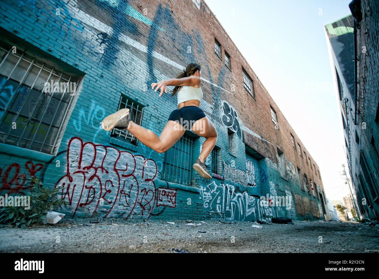 Female athlete running along street past blue building covered in ...