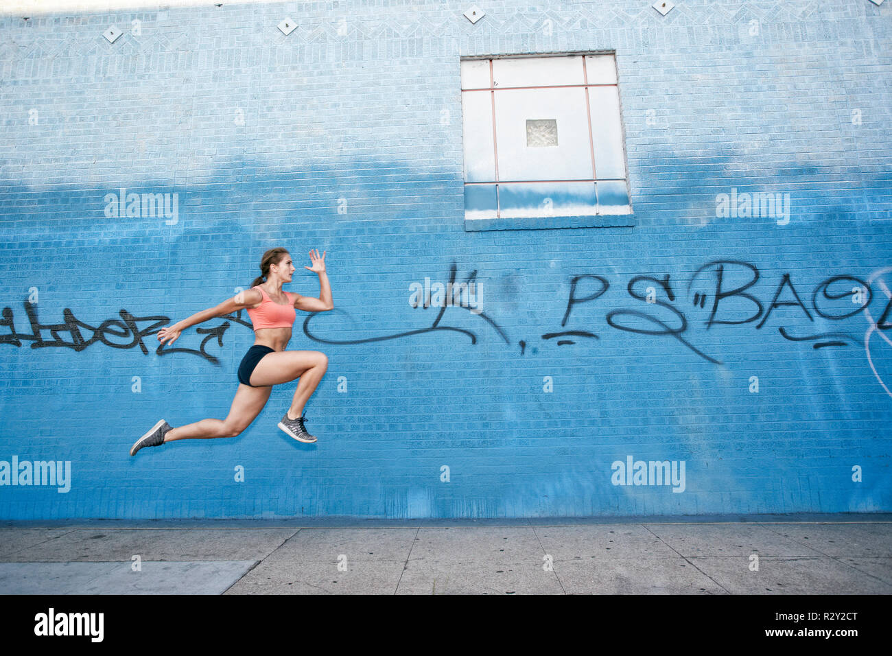 Female athlete running along sidewalk past blue building covered in ...