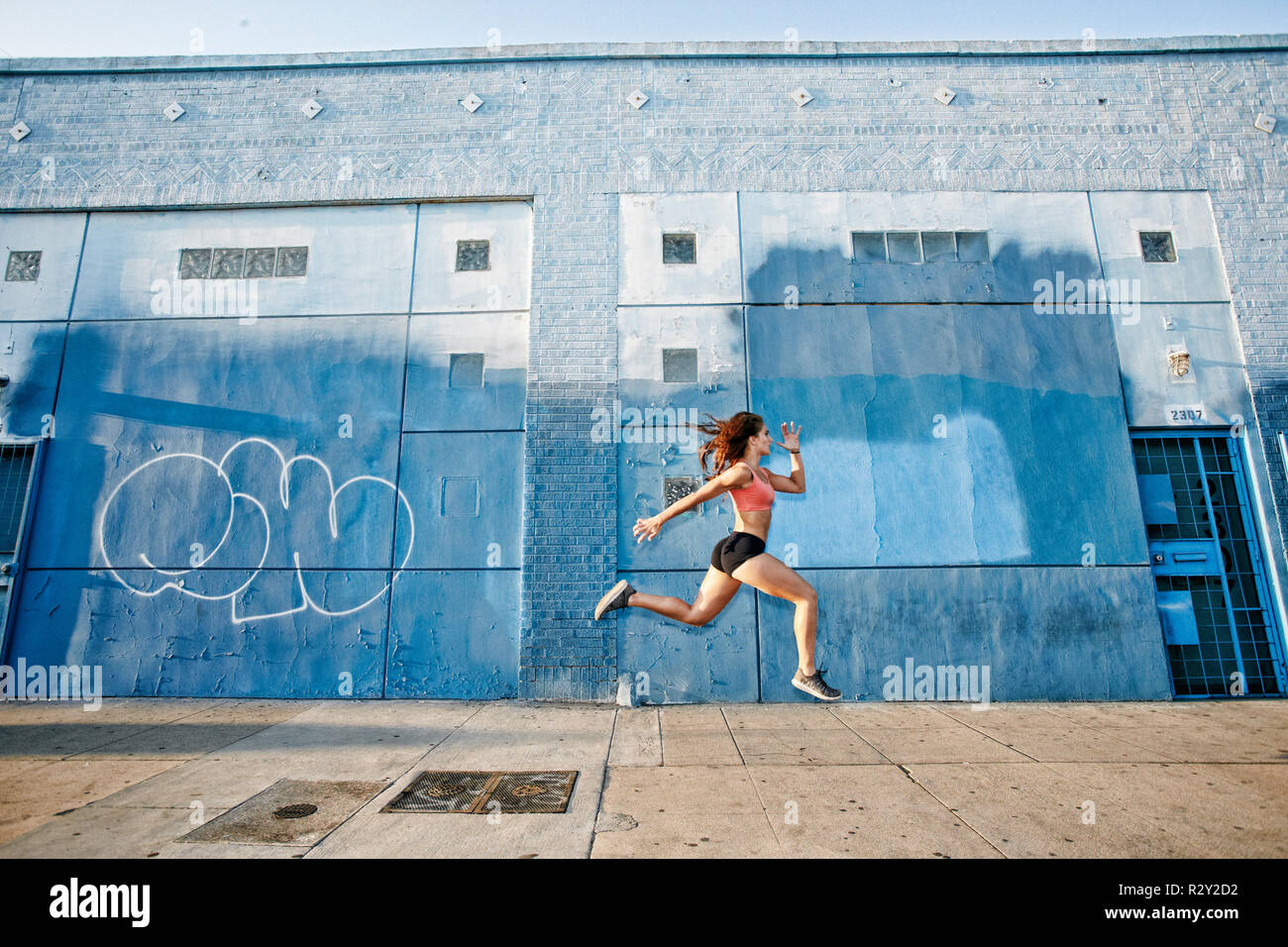 Female athlete running along sidewalk past blue building covered in ...