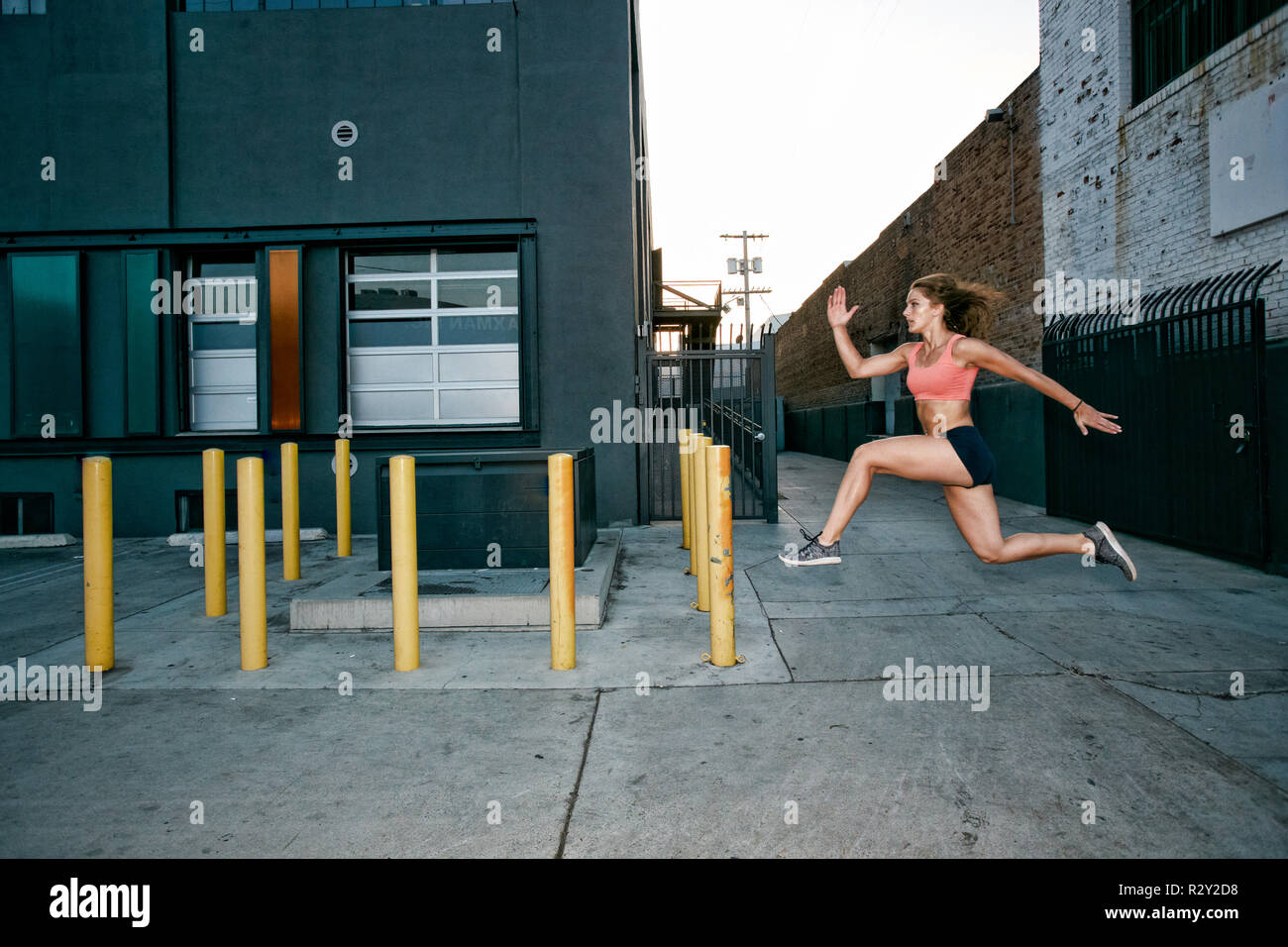 Female athlete running on sidewalk past industrial buildings Stock ...