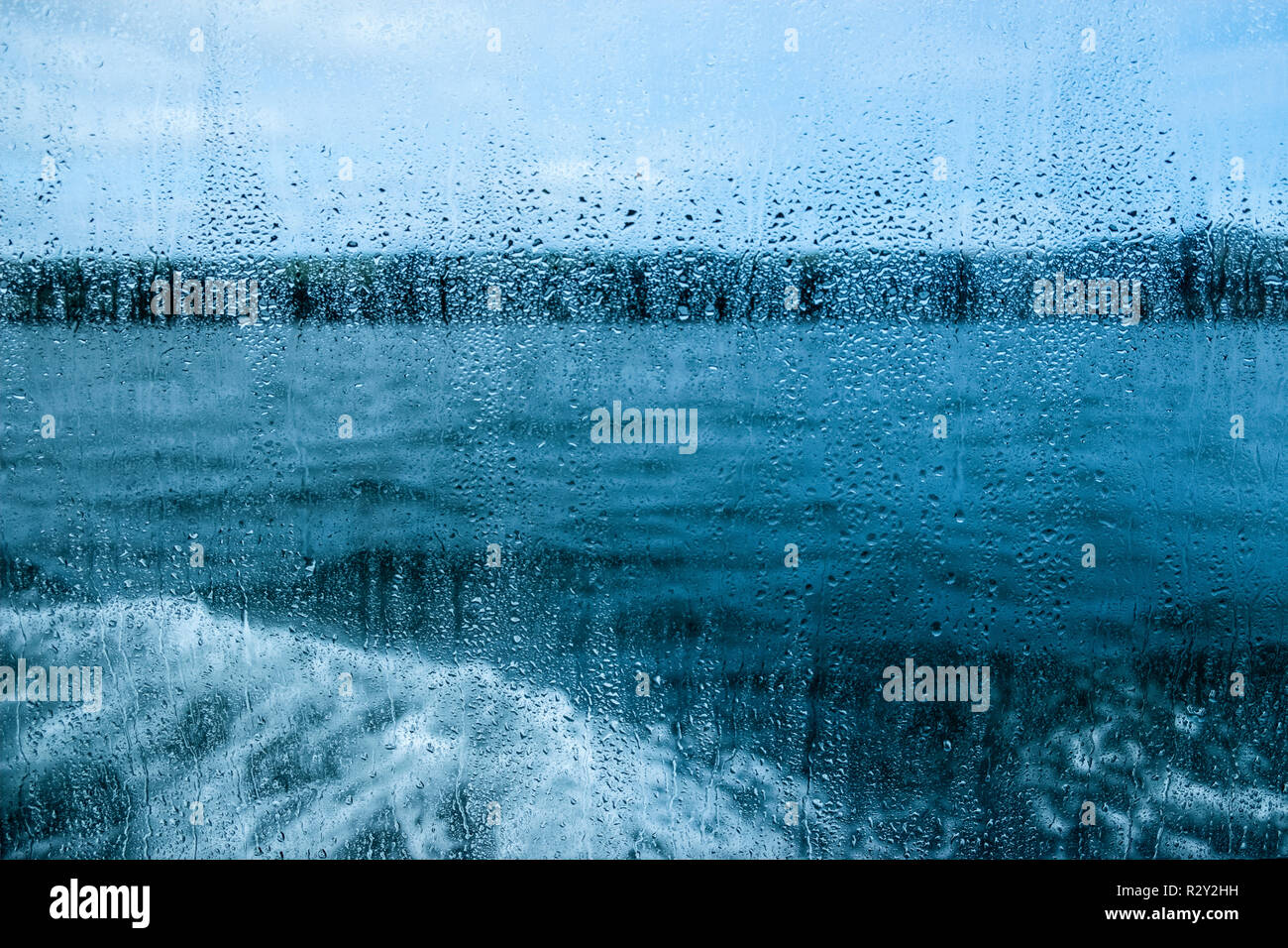 View through a rain spattered window over water and a boat's wake on an ...