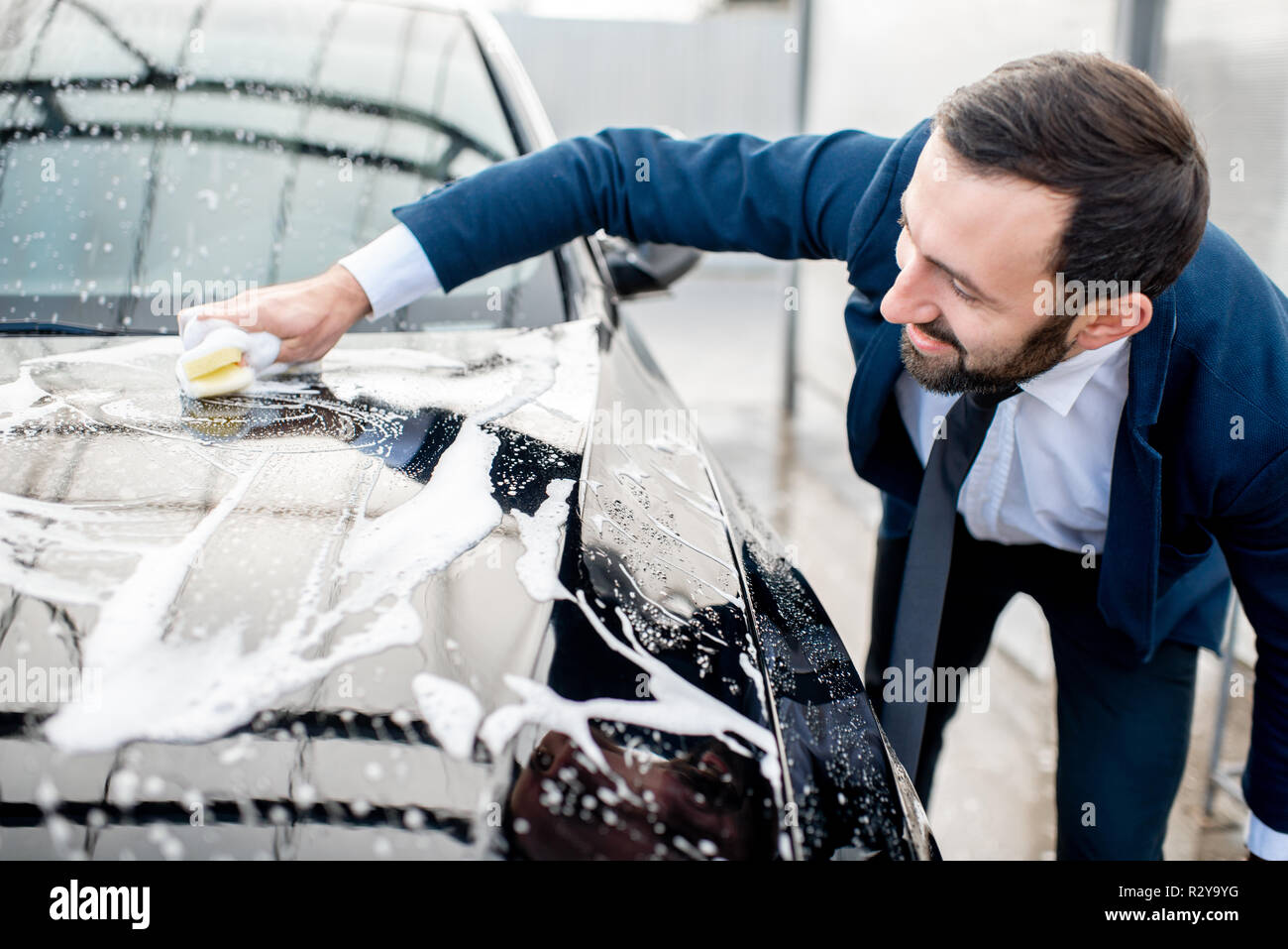 Elegant businessman dressed in the suit washing his car with yellow ...