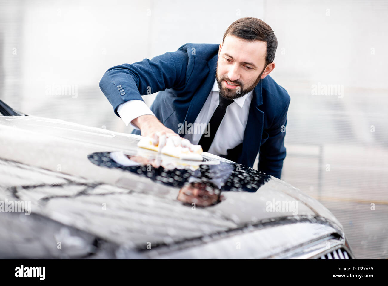 Elegant businessman dressed in the suit washing his car with yellow ...