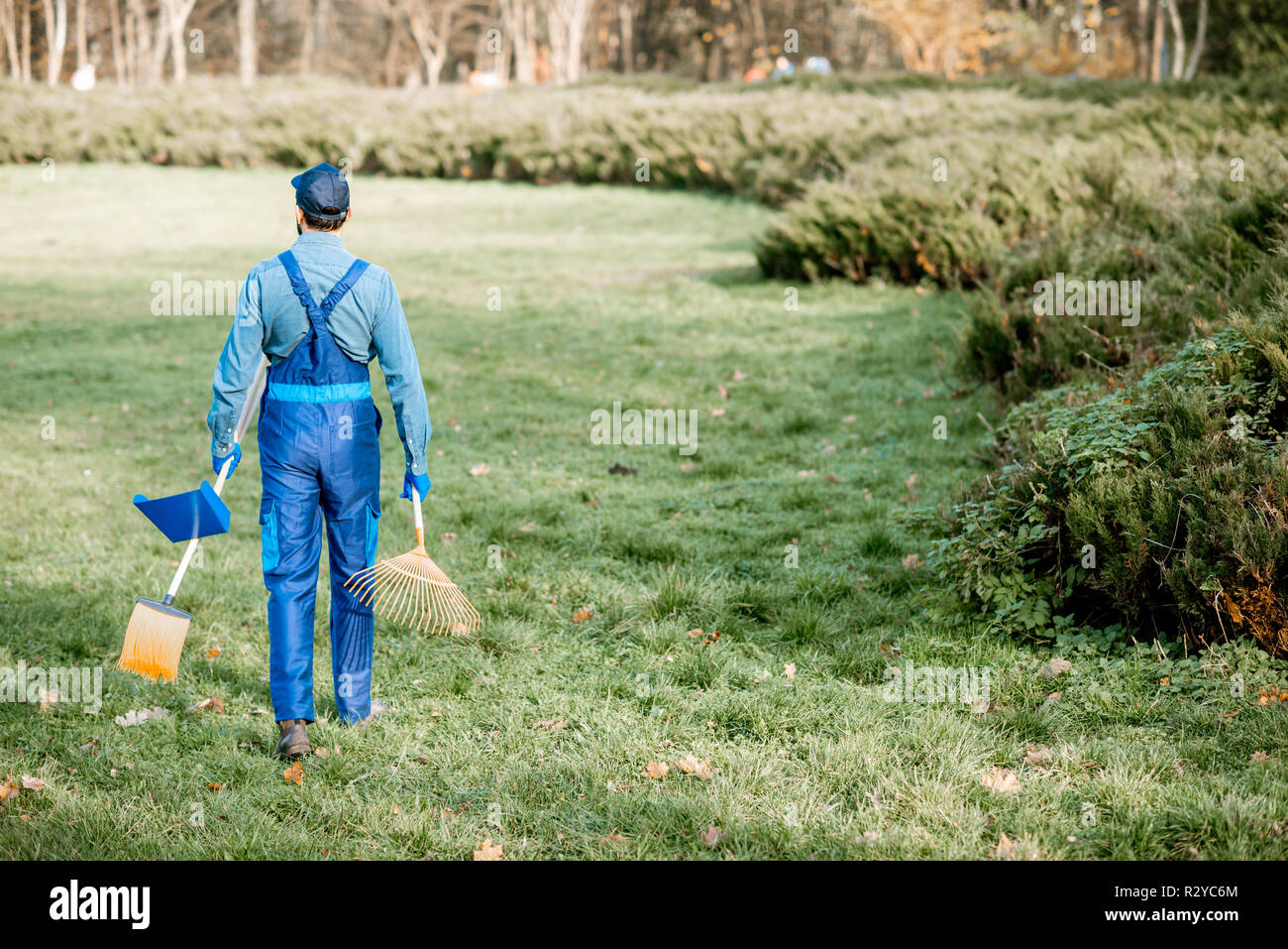 Professional sweeper or gardener in working uniform walking with ...