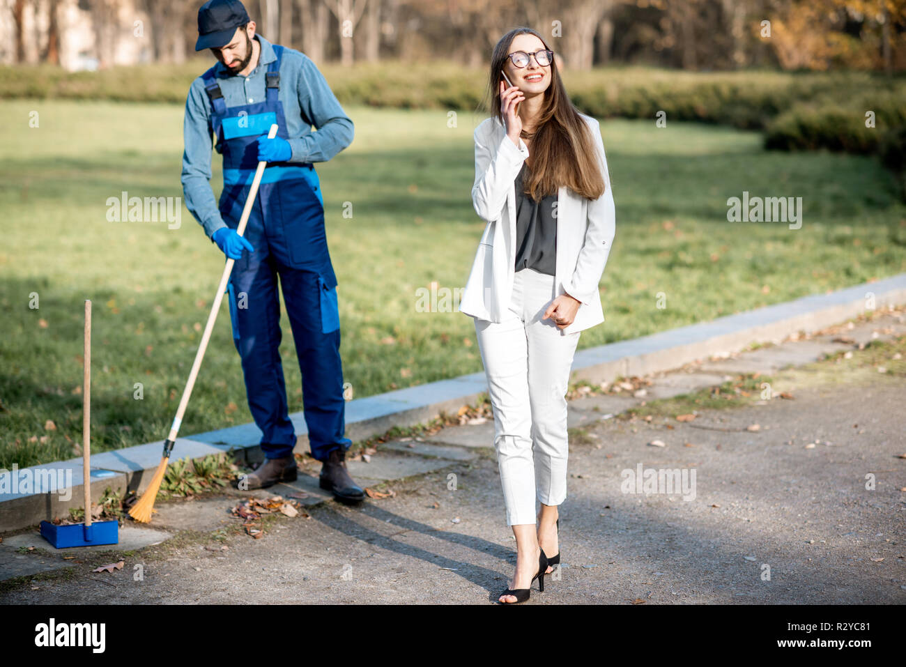 Elegant businesswoman walking through the man sweeping the street with ...