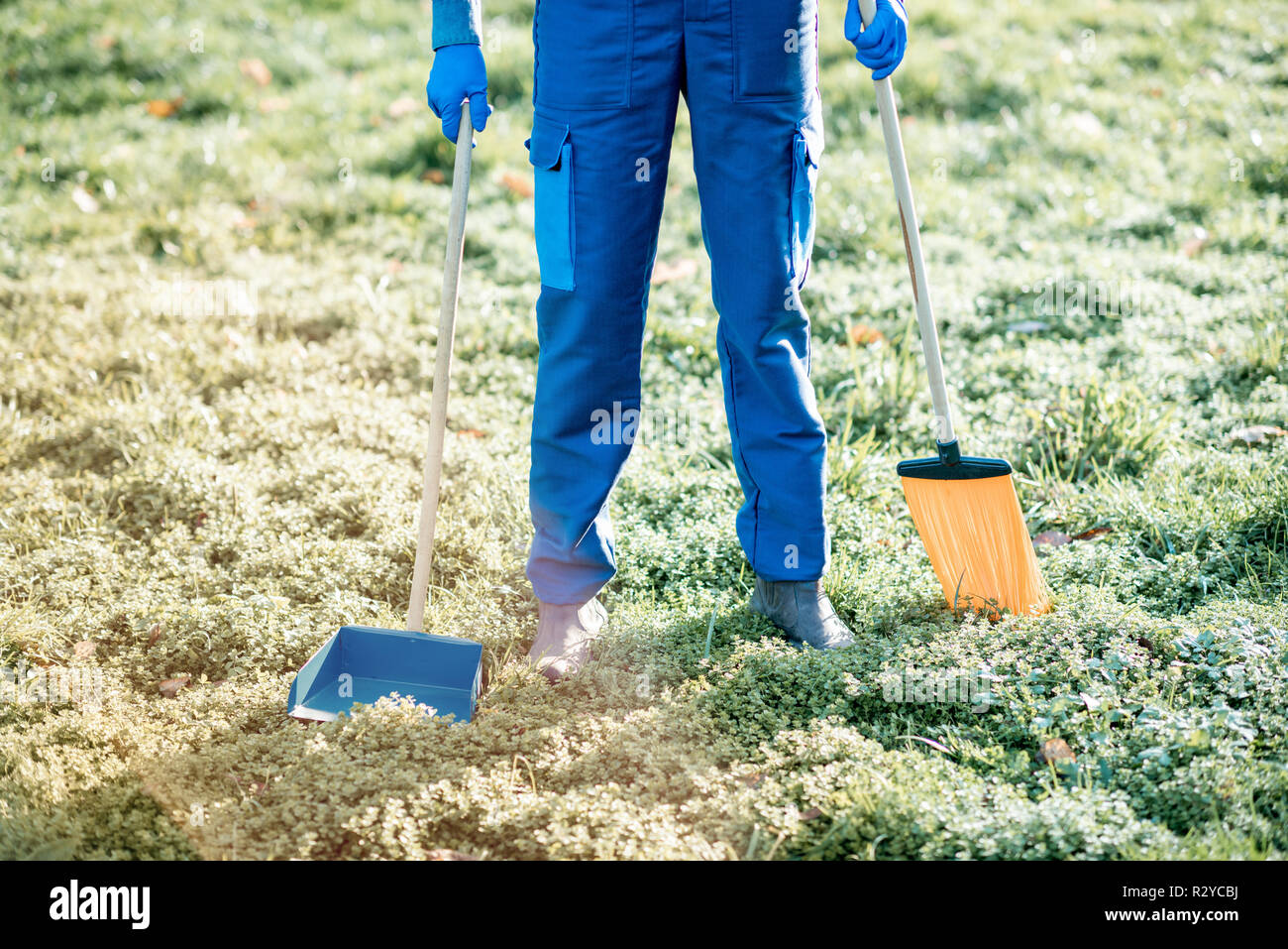 Sweeper in uniform with cleaning tools in the garden, cropped image ...