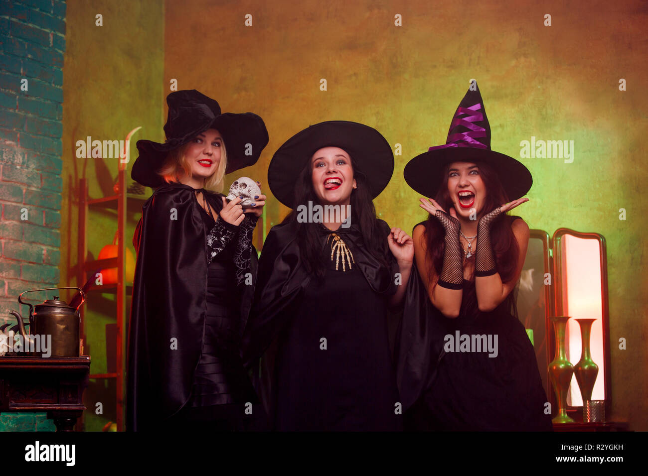 Portrait of three witches in black hats in dark room on background of ...