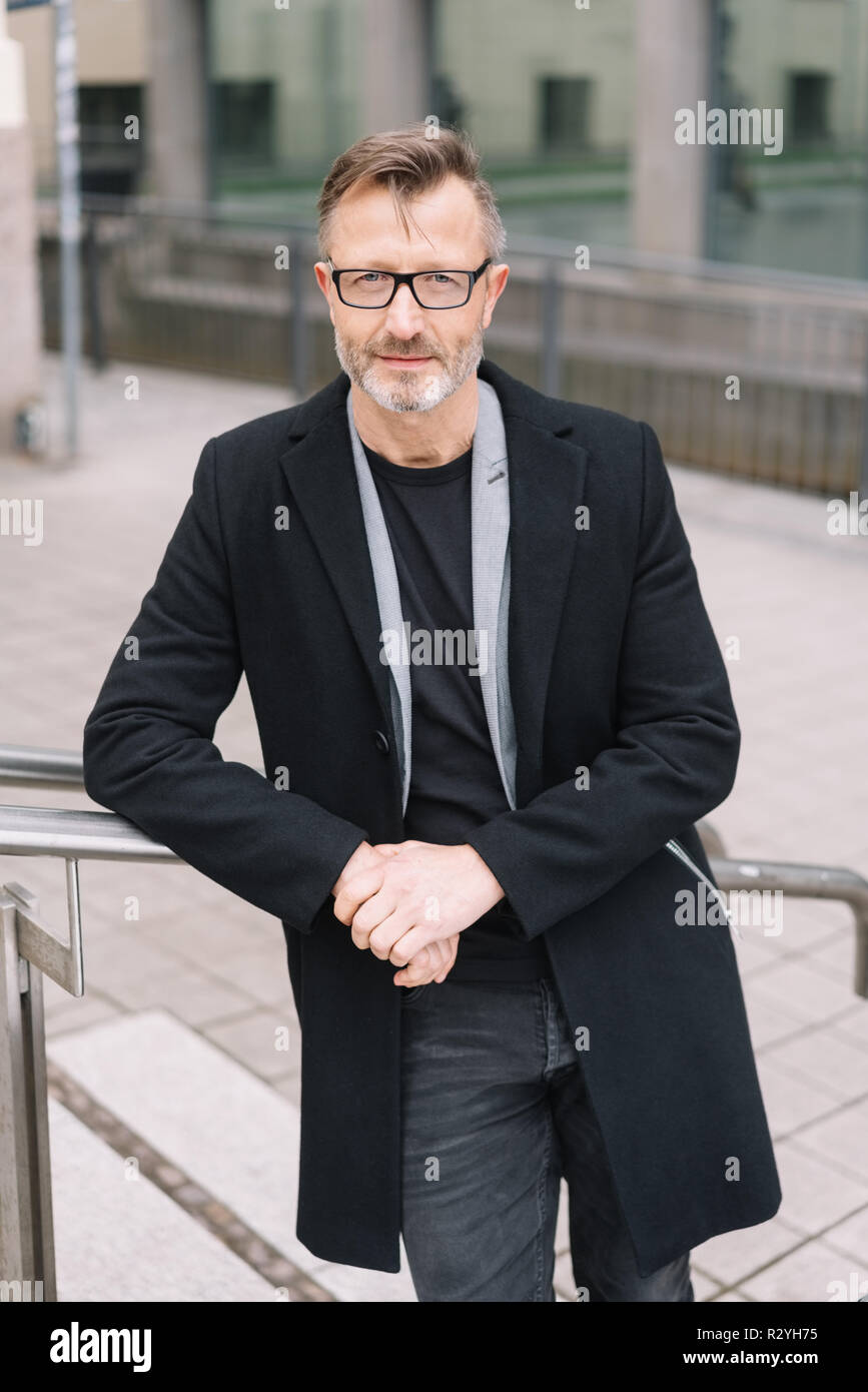Street Portrait Of Mature Bearded Man With Glasses Wearing Black Coat