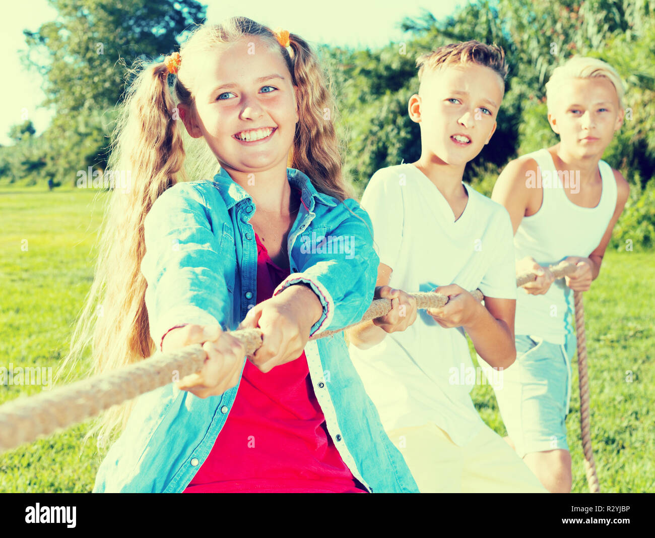 Group of laughing children having fun together outdoors pulling rope ...
