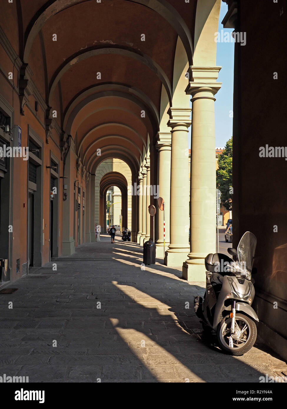 sunlit scooter parked in arched arcade with oblique shadows of pillars ...