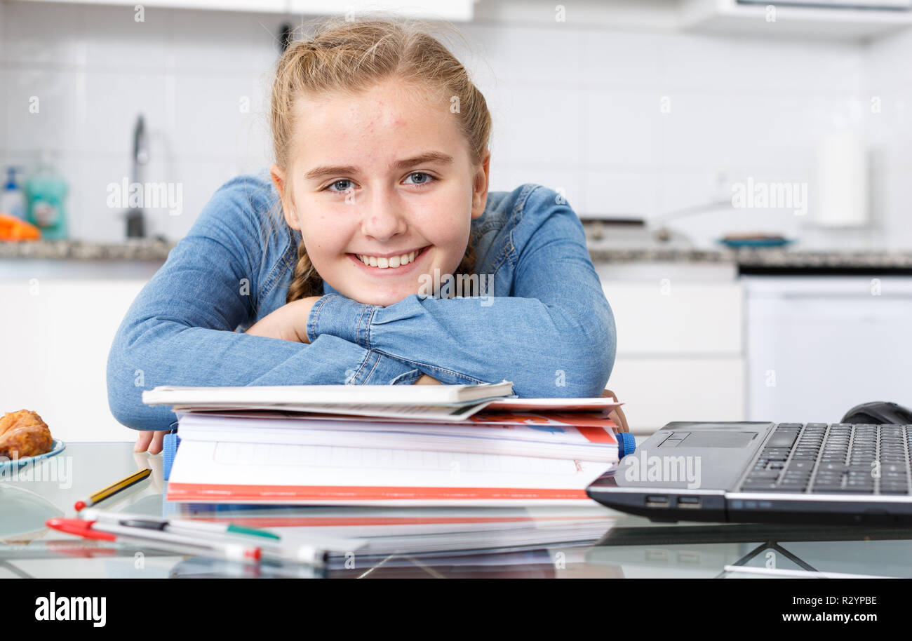 Happy teenage girl sitting at kitchen table among notebooks and ...