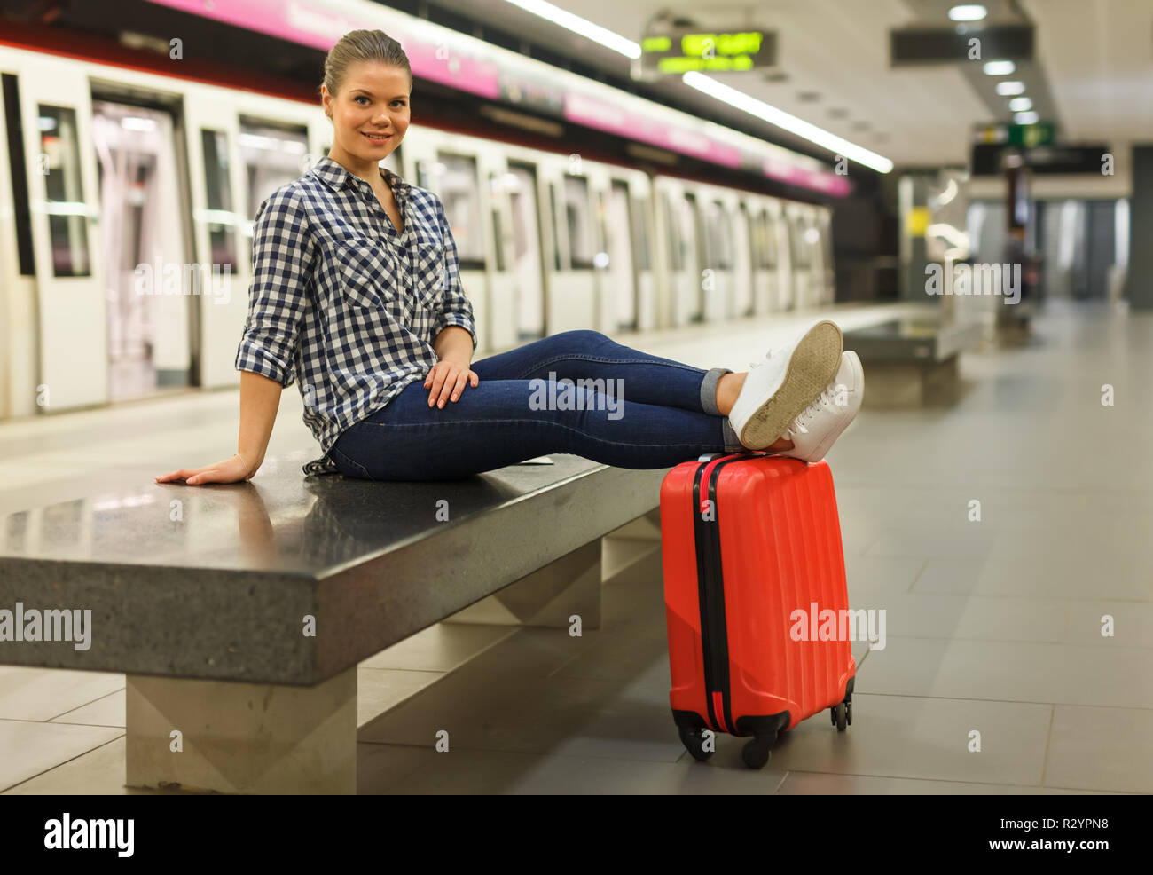 Joyful girl traveler waiting for train at metro station sitting on ...