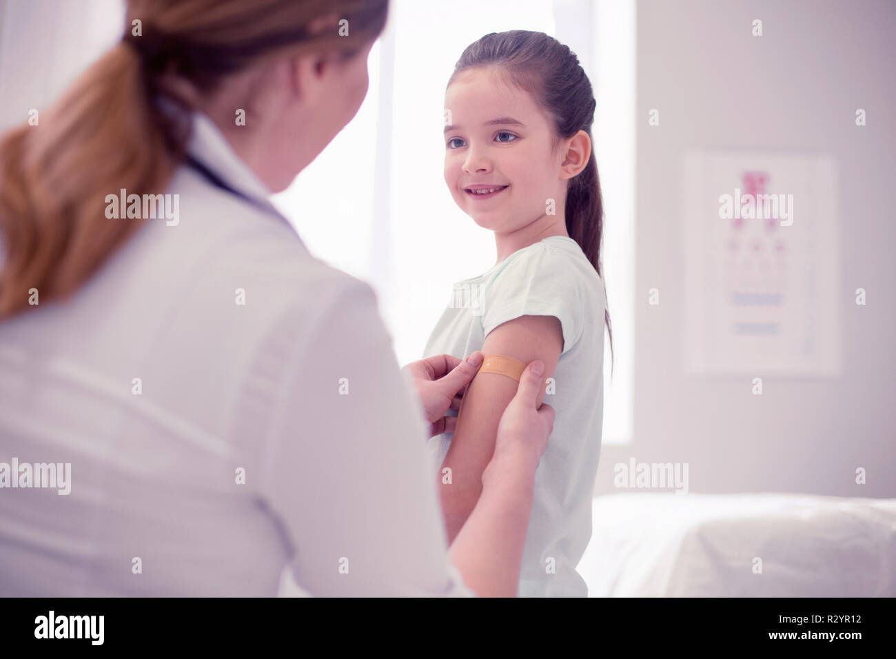 Doctor wearing white jacket putting sticking plaster on hand of girl ...