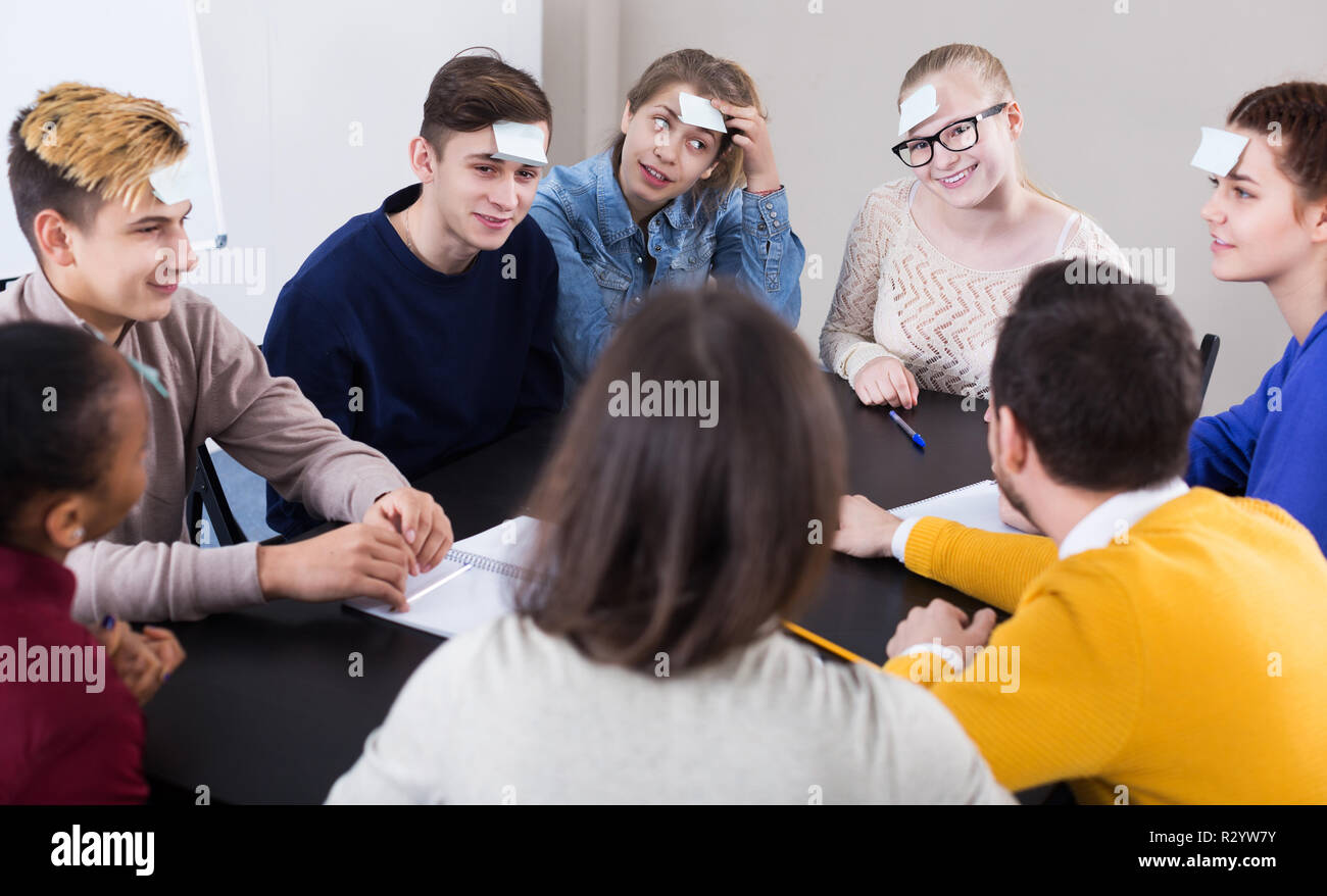 Hapy young male and female students playing guess-who game in school ...