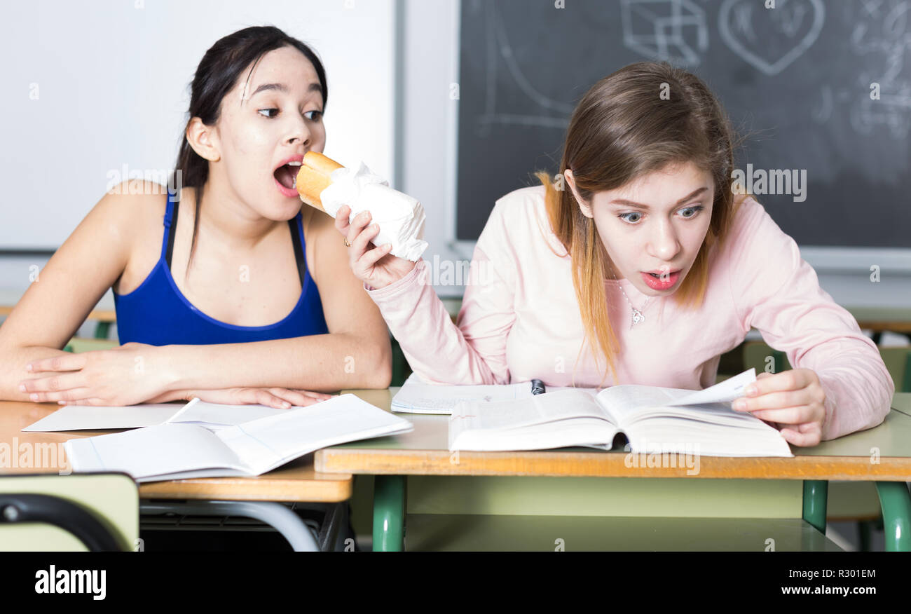 Two girls are eating sandwich at the desk and writing homework in the ...