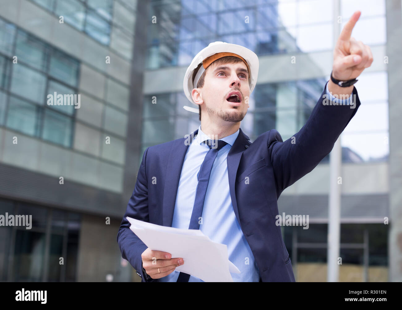 Man in helmet with documents pointing finger to object Stock Photo - Alamy