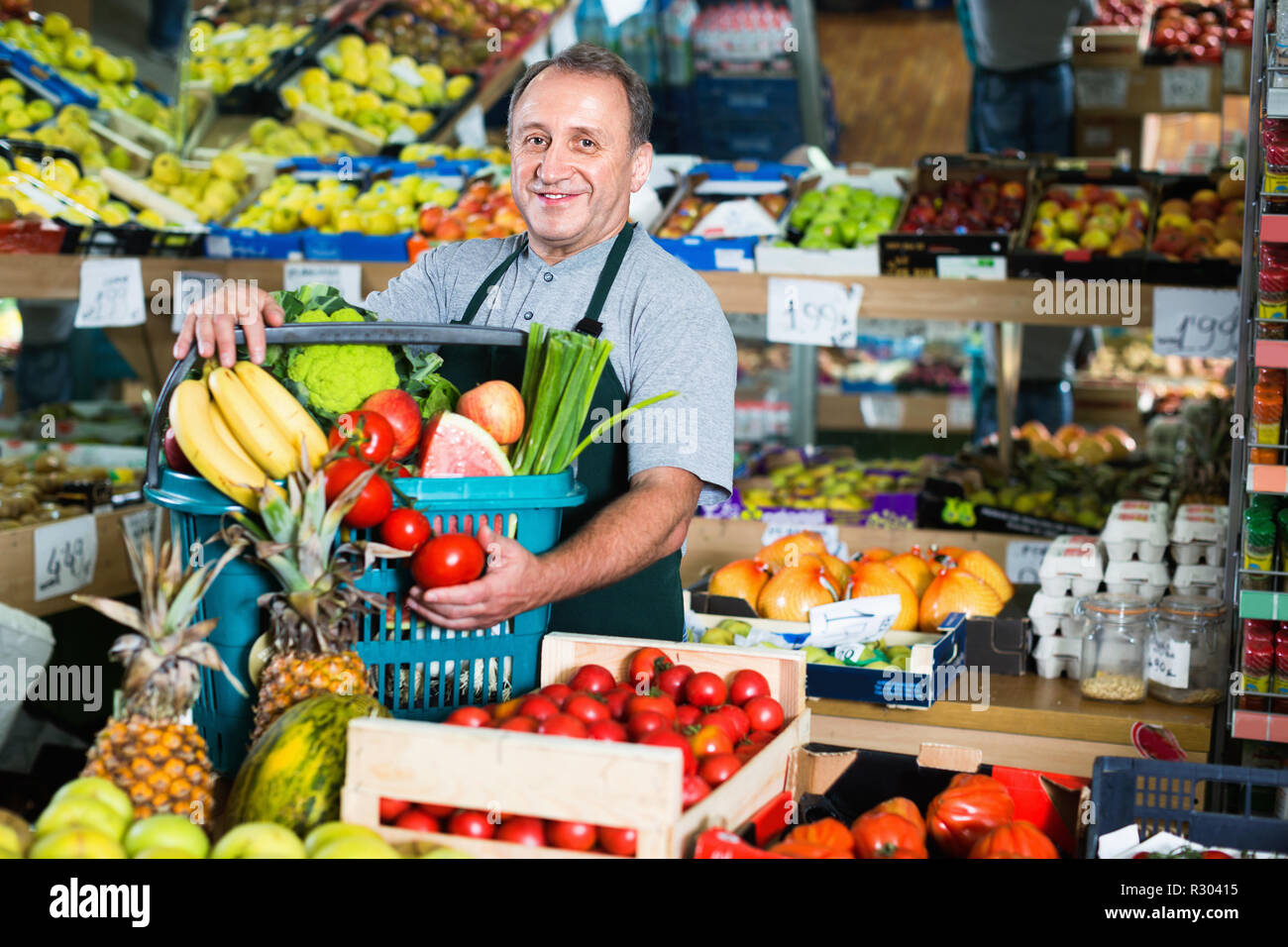 Smiling positive glad man seller is standing with basket with fruits ...