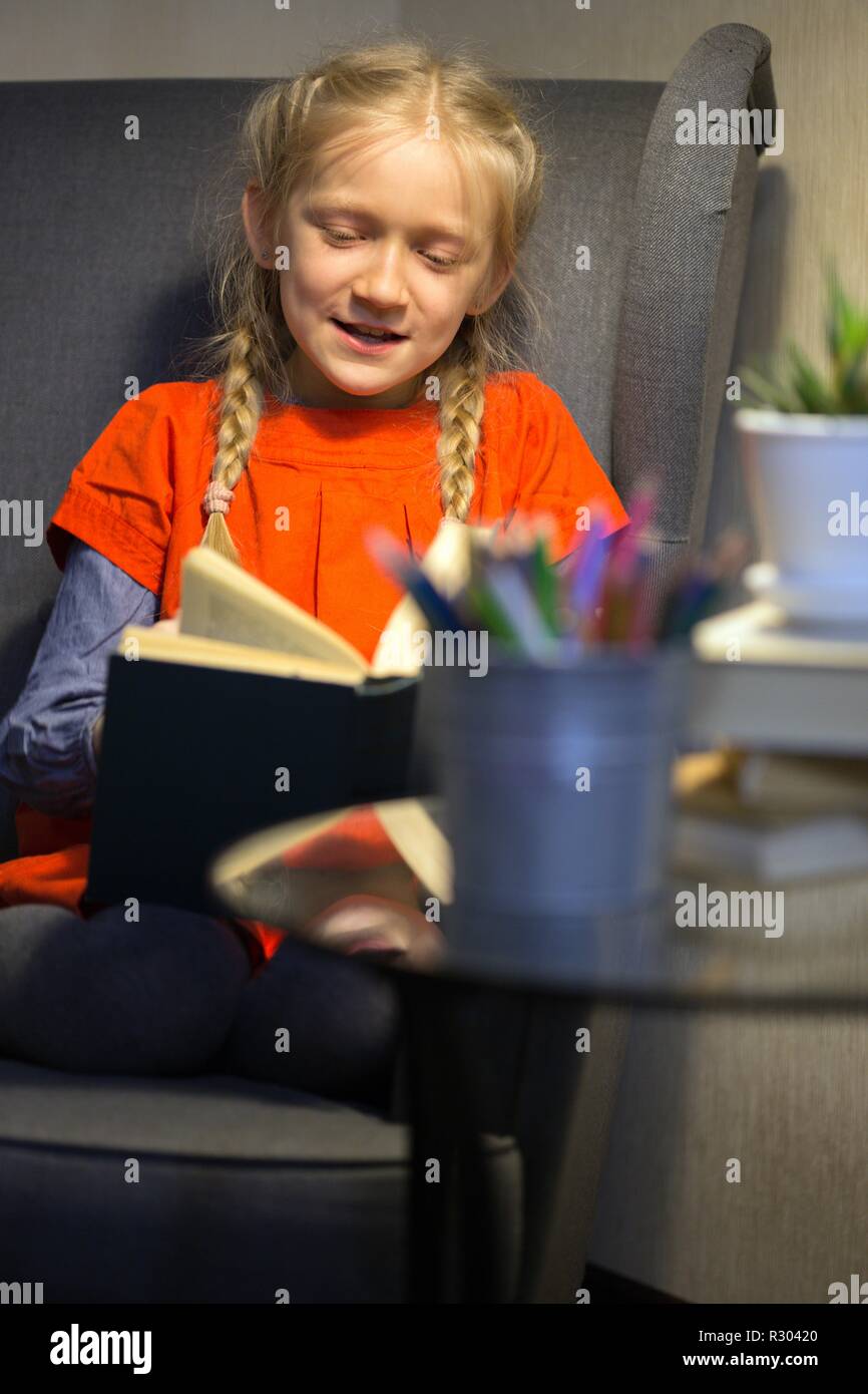 little girl is sitting in a chair and is reading a book Stock Photo - Alamy