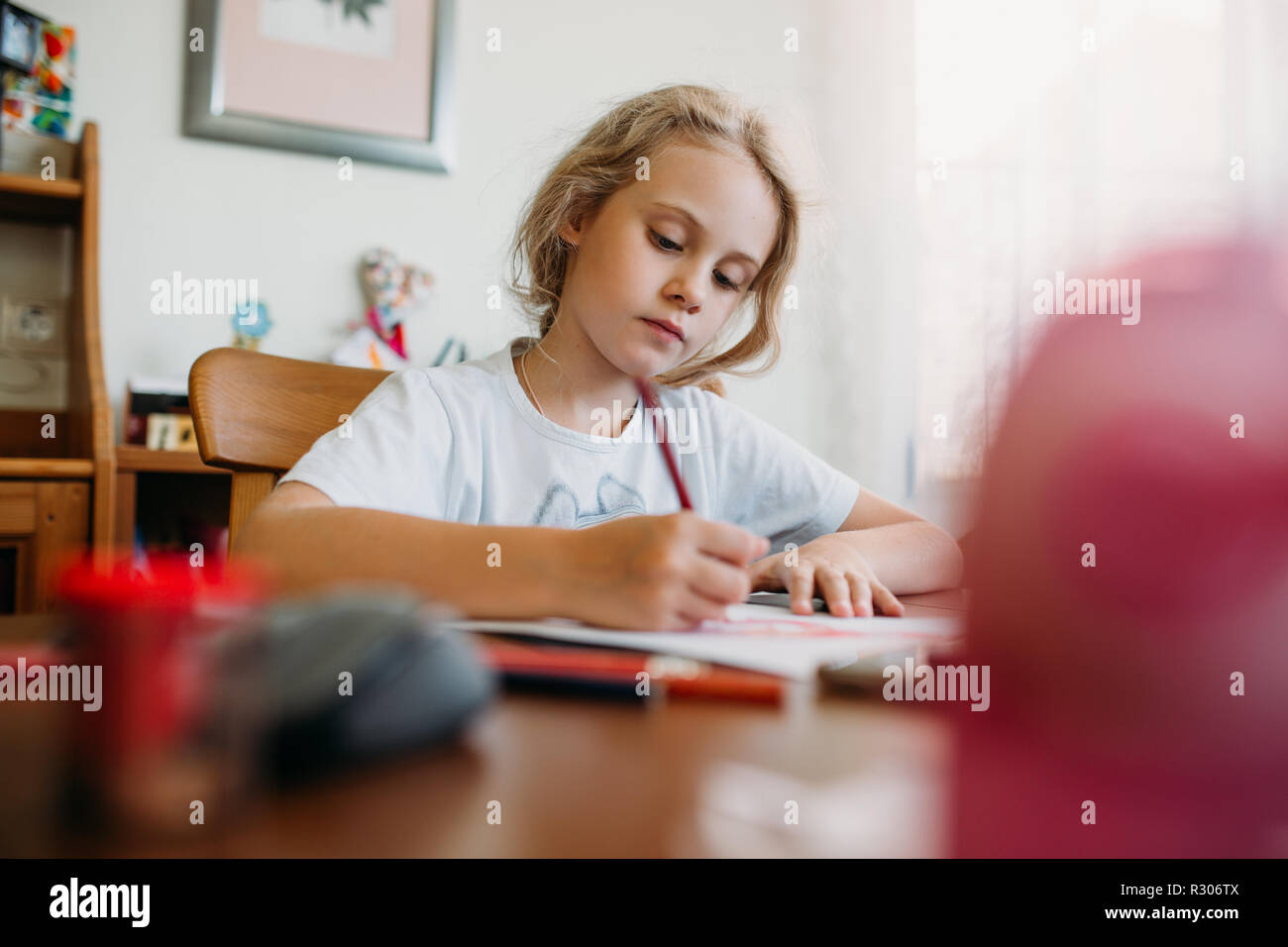 A seven-year-old girl sits at home at a table and writes in a notebook ...