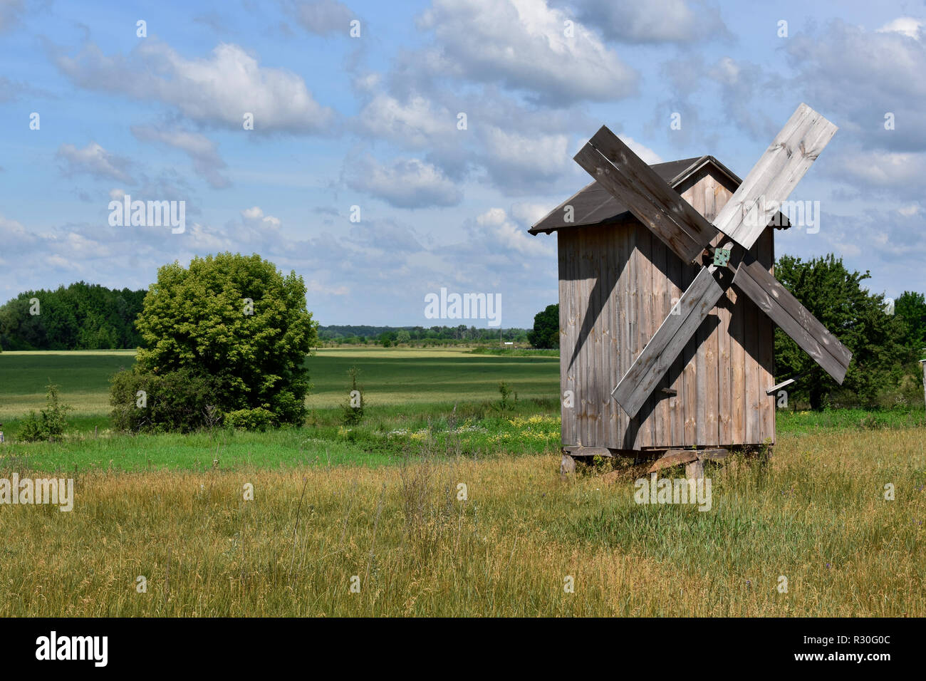 An abandoned wooden windmill in the vast green field near the forest ...