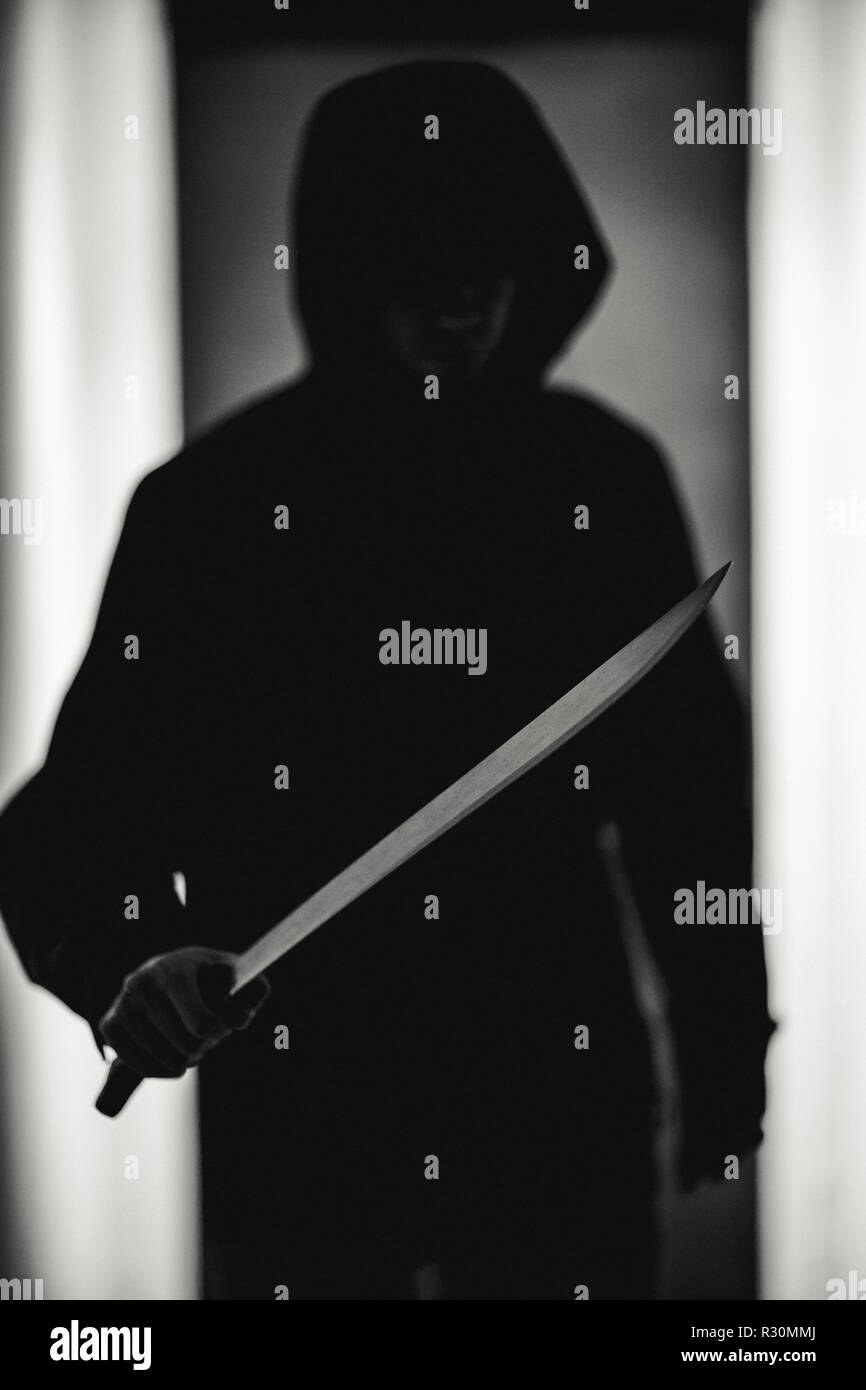 Black and white photo of criminal in hood with machete in dark room ...