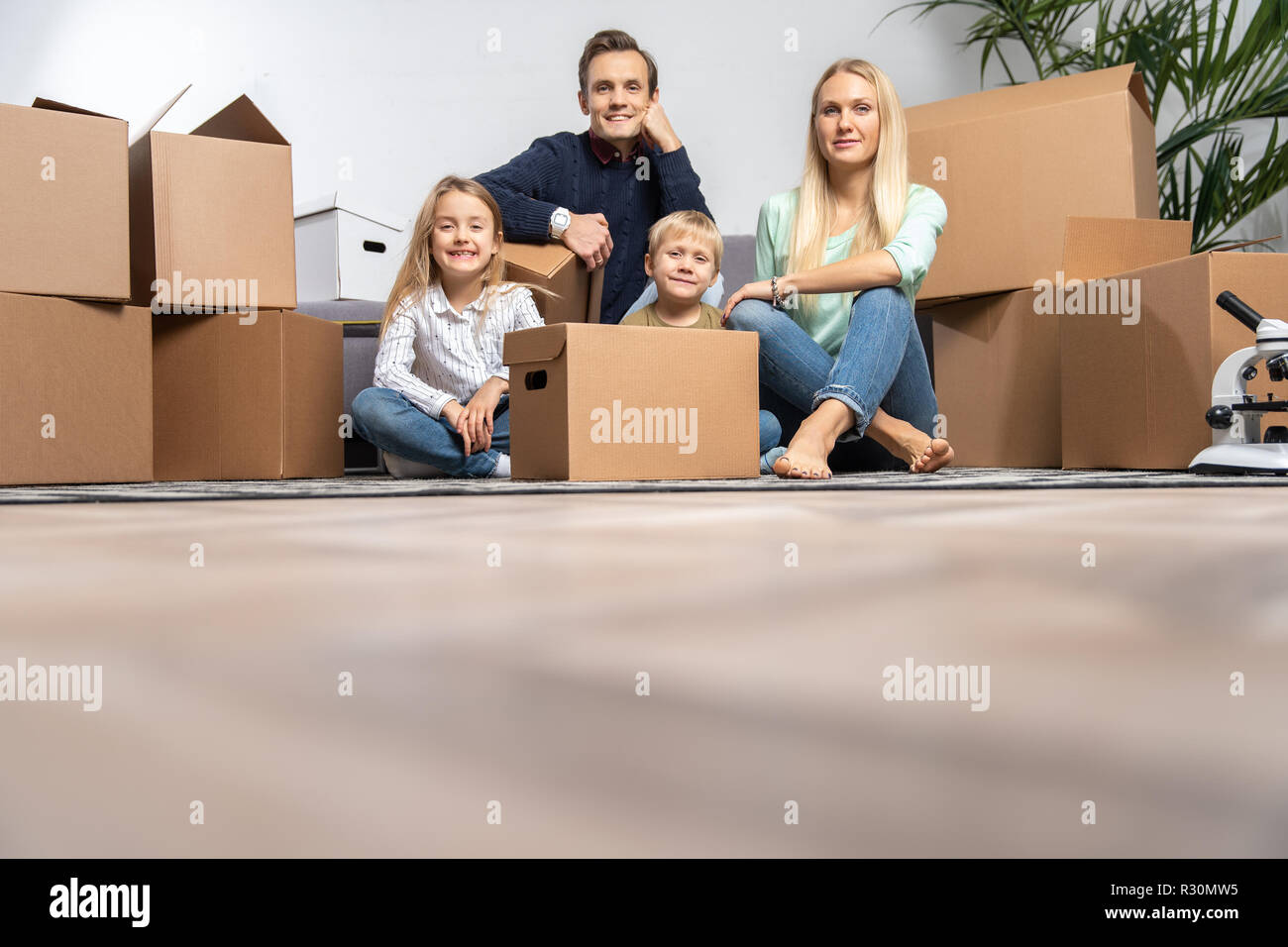 Photo of parents and children among cardboard boxes sitting on floor in ...