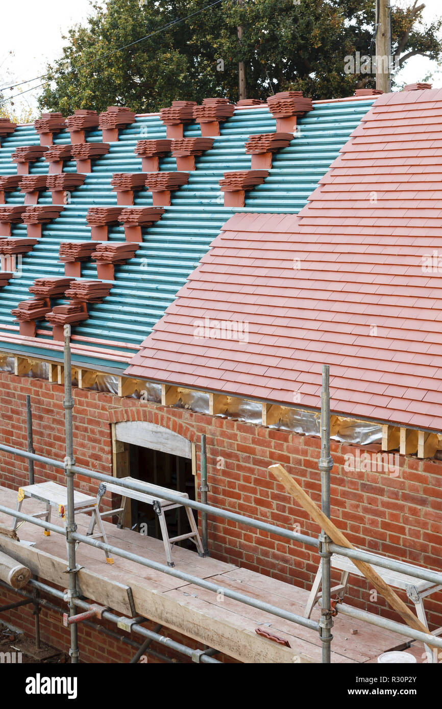 A roof on a building site in the process of being tiled with plain clay ...