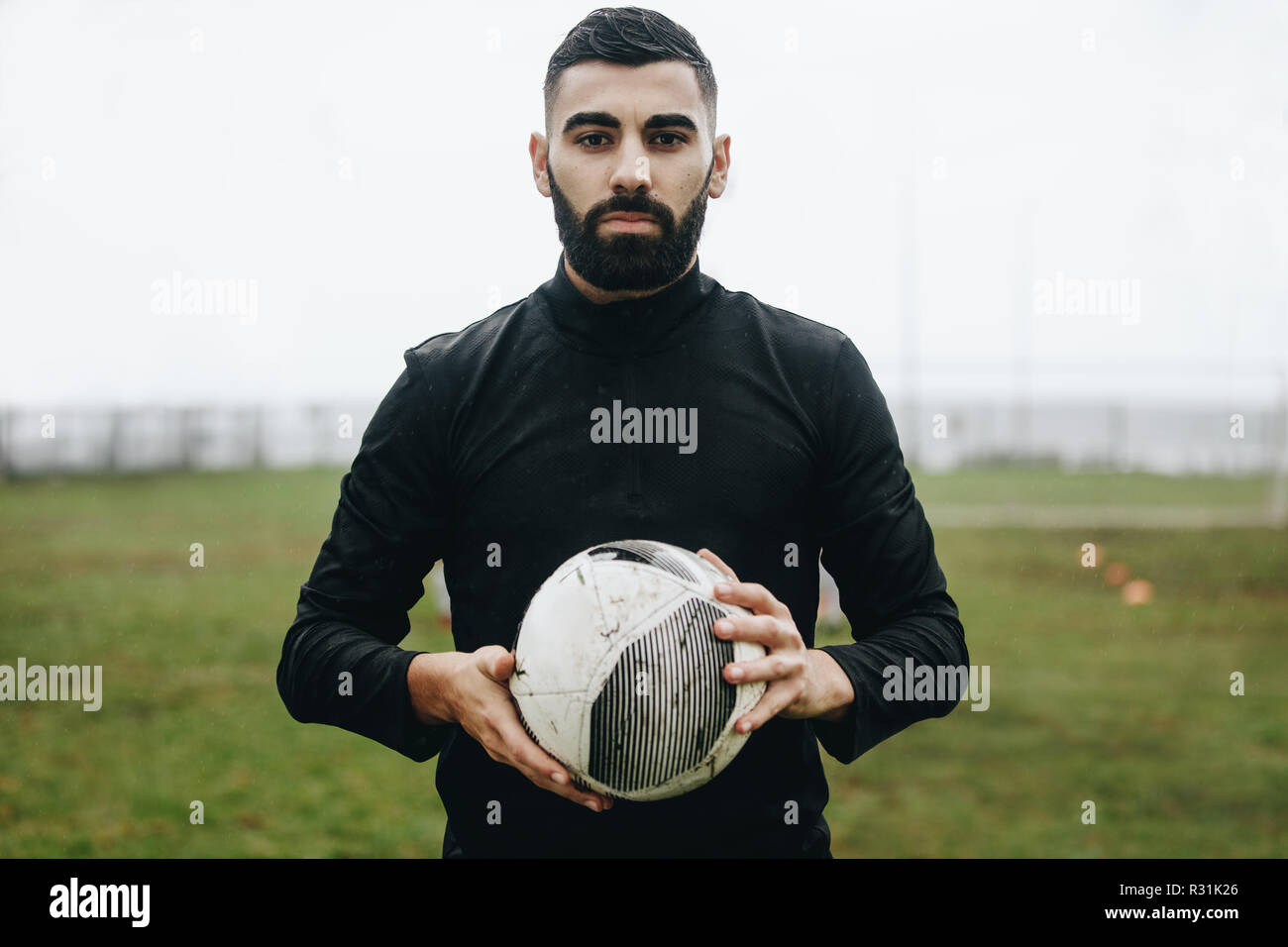 football player standing on field holding a football in hand. Man ...