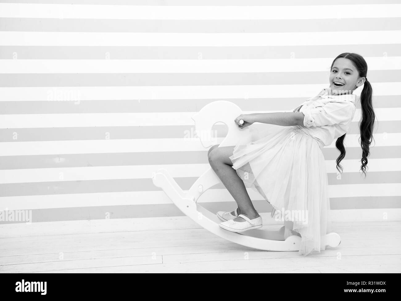 Have fun. Girl child rides white rocking horse on striped background ...