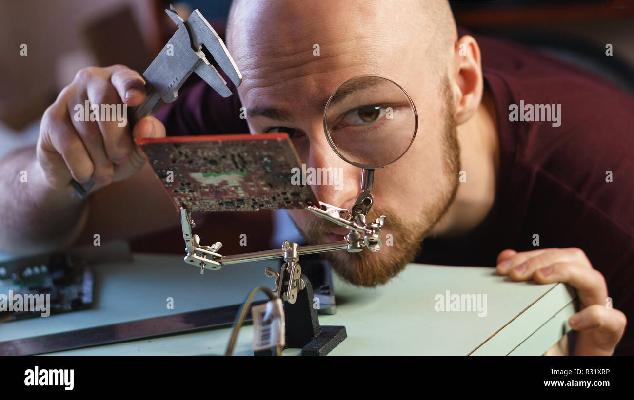 Repair motherboard. Service technician looks through magnifying glass ...