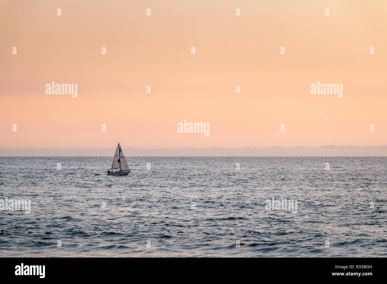 Small sailboat in the distance heading towards the sun of an orange and ...