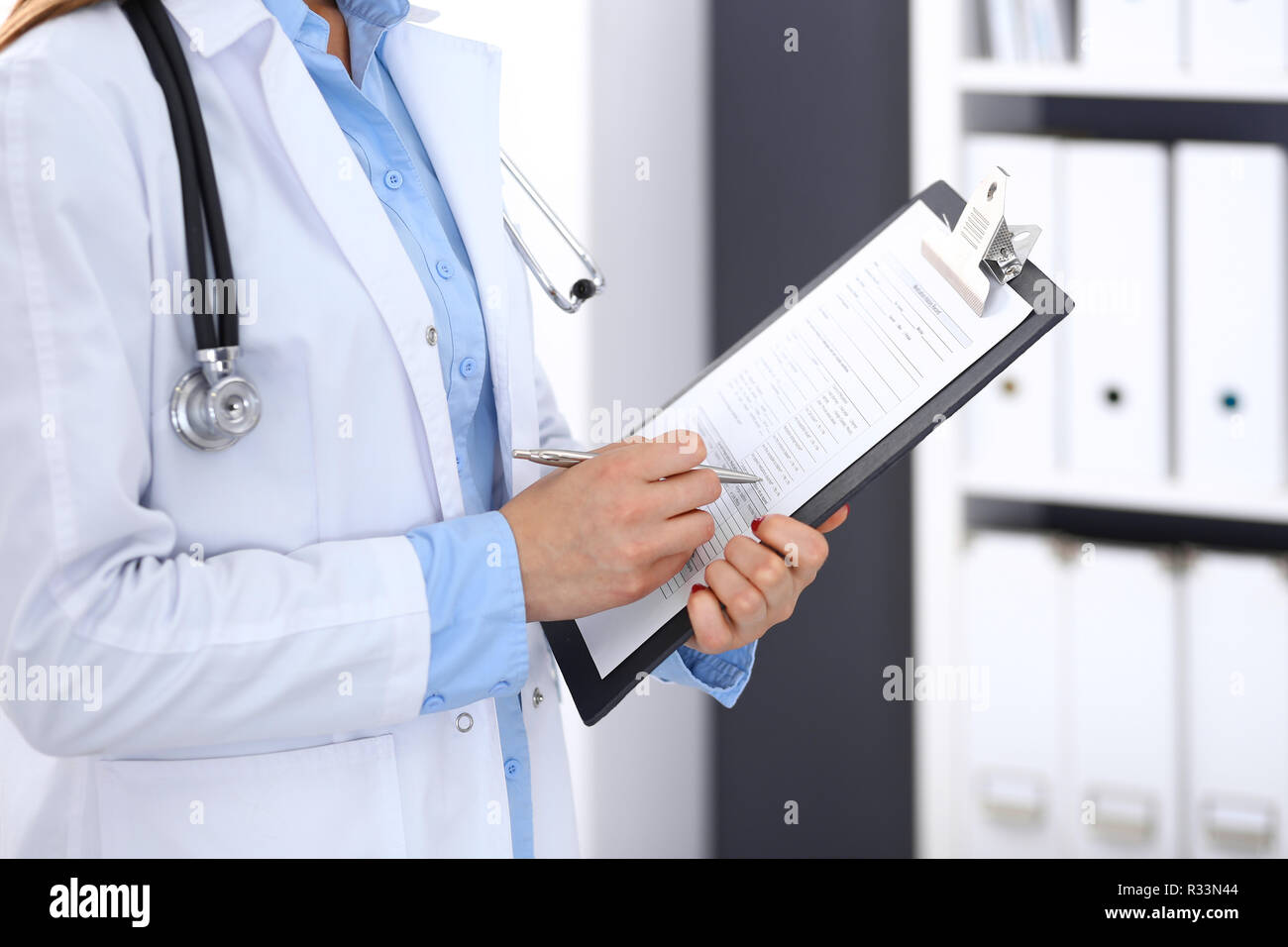 Unknown doctor woman filling up medical form in hospital office, close ...