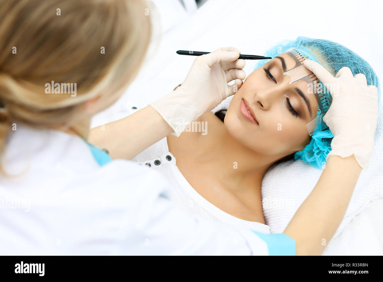 Professional beautician is going to correct eyebrow line at woman face ...